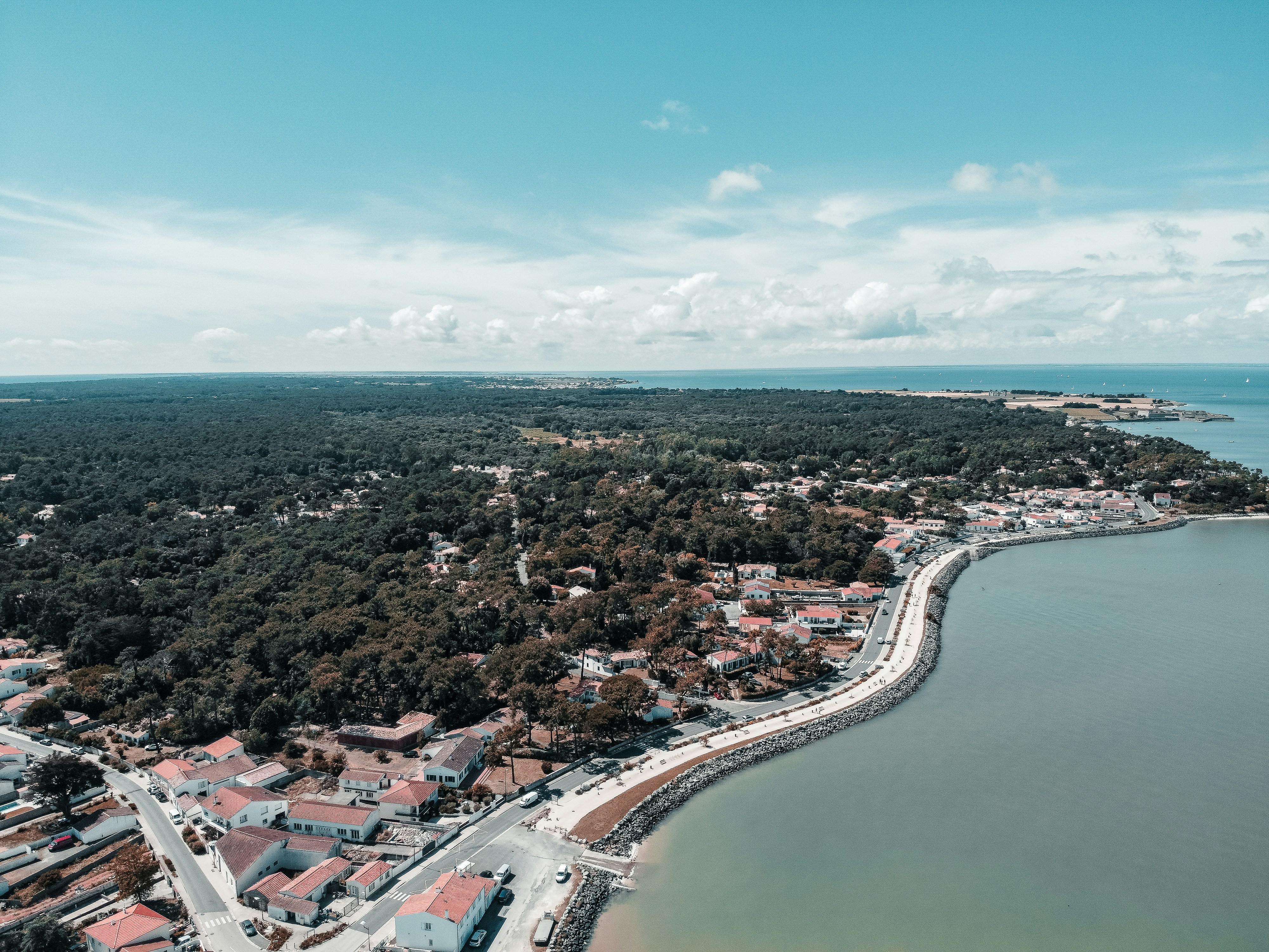 Aerial view of a coastal town nestled between lush greenery and tranquil waters, showcasing the harmonious blend of nature and human settlement.