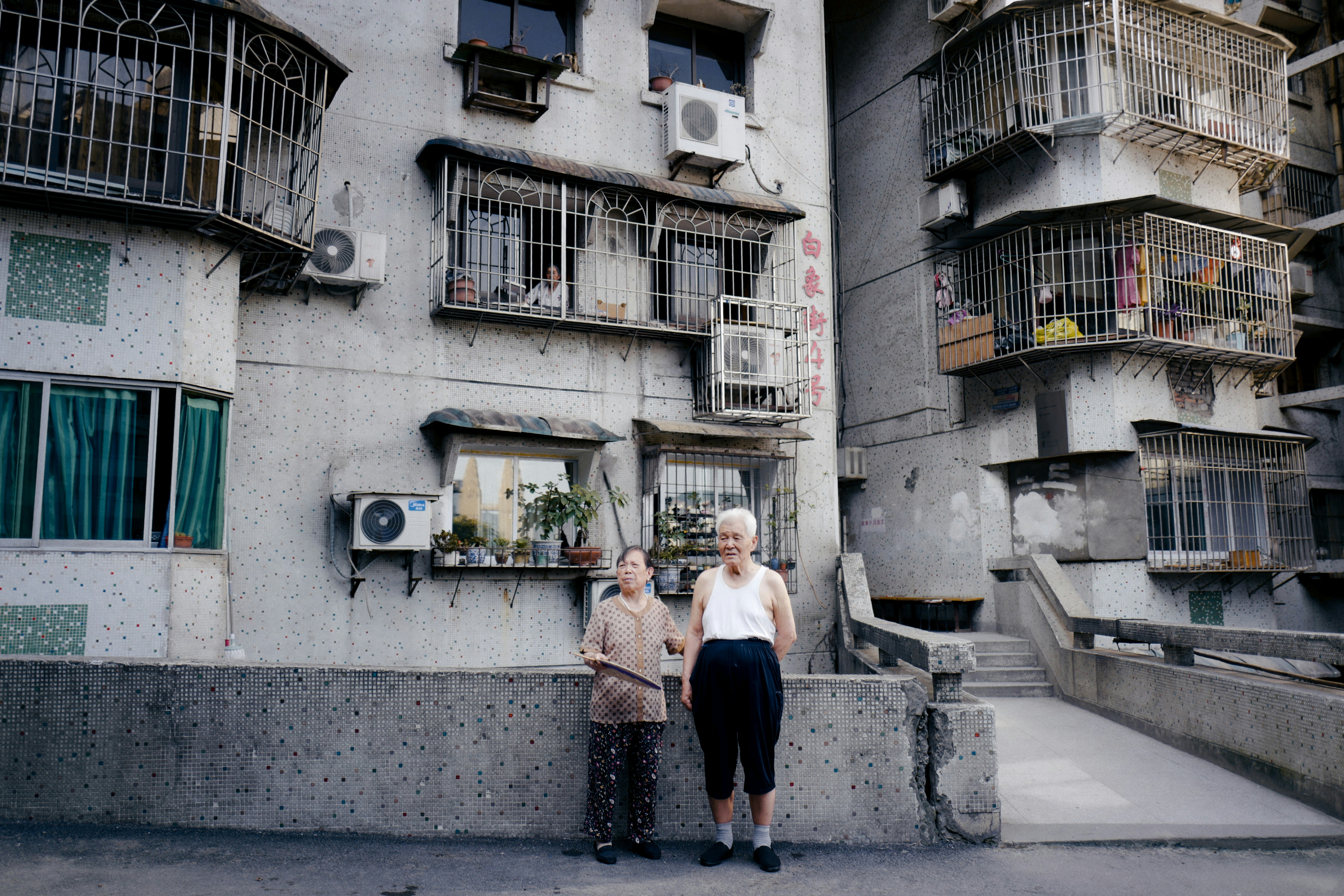 Two elderly women stand together in front of a weathered apartment building, showcasing the character of urban living. The architecture reflects a blend of functionality and history.