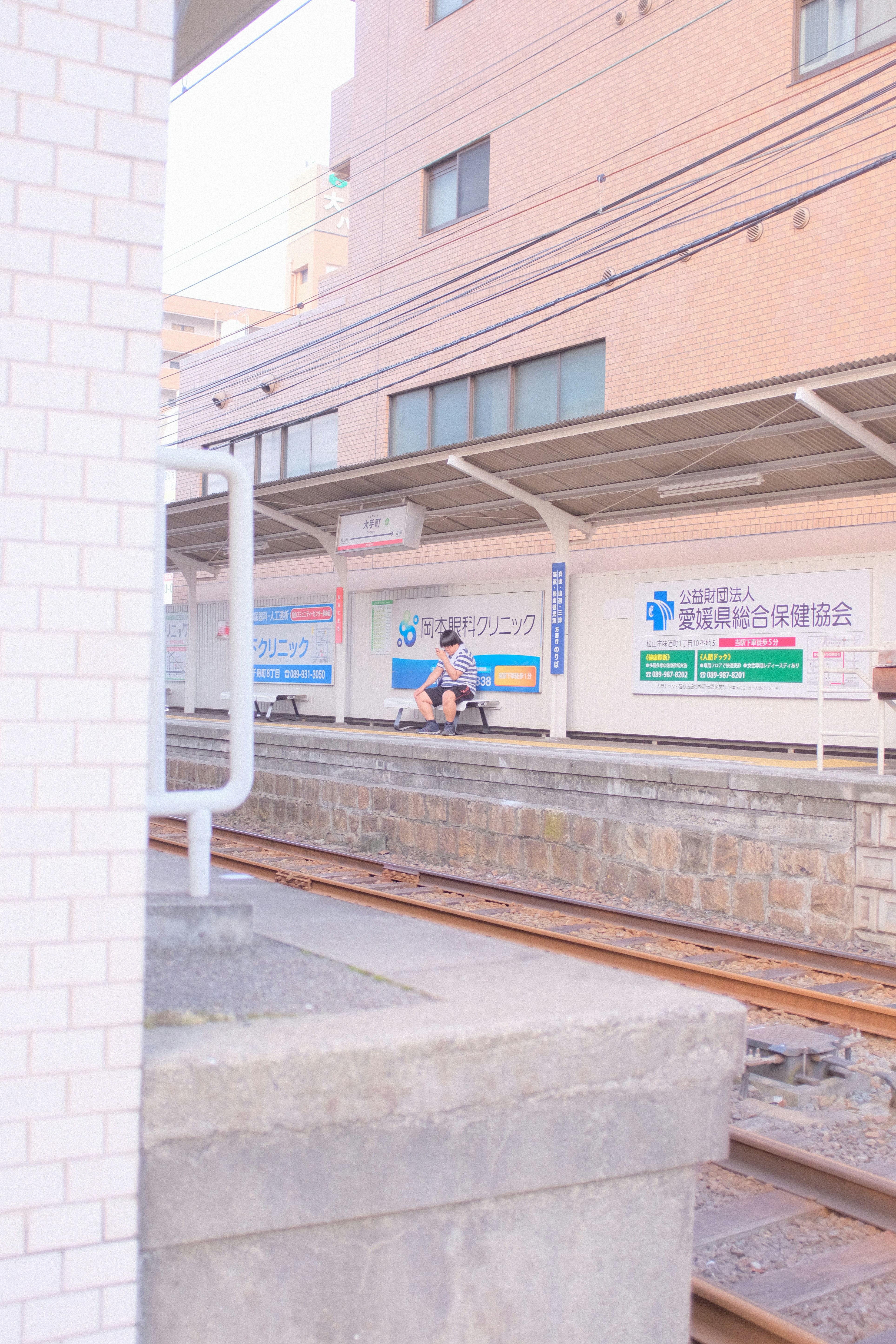 A lone figure sits on a bench at a train station, surrounded by colorful advertisements and the quiet ambiance of the platform.