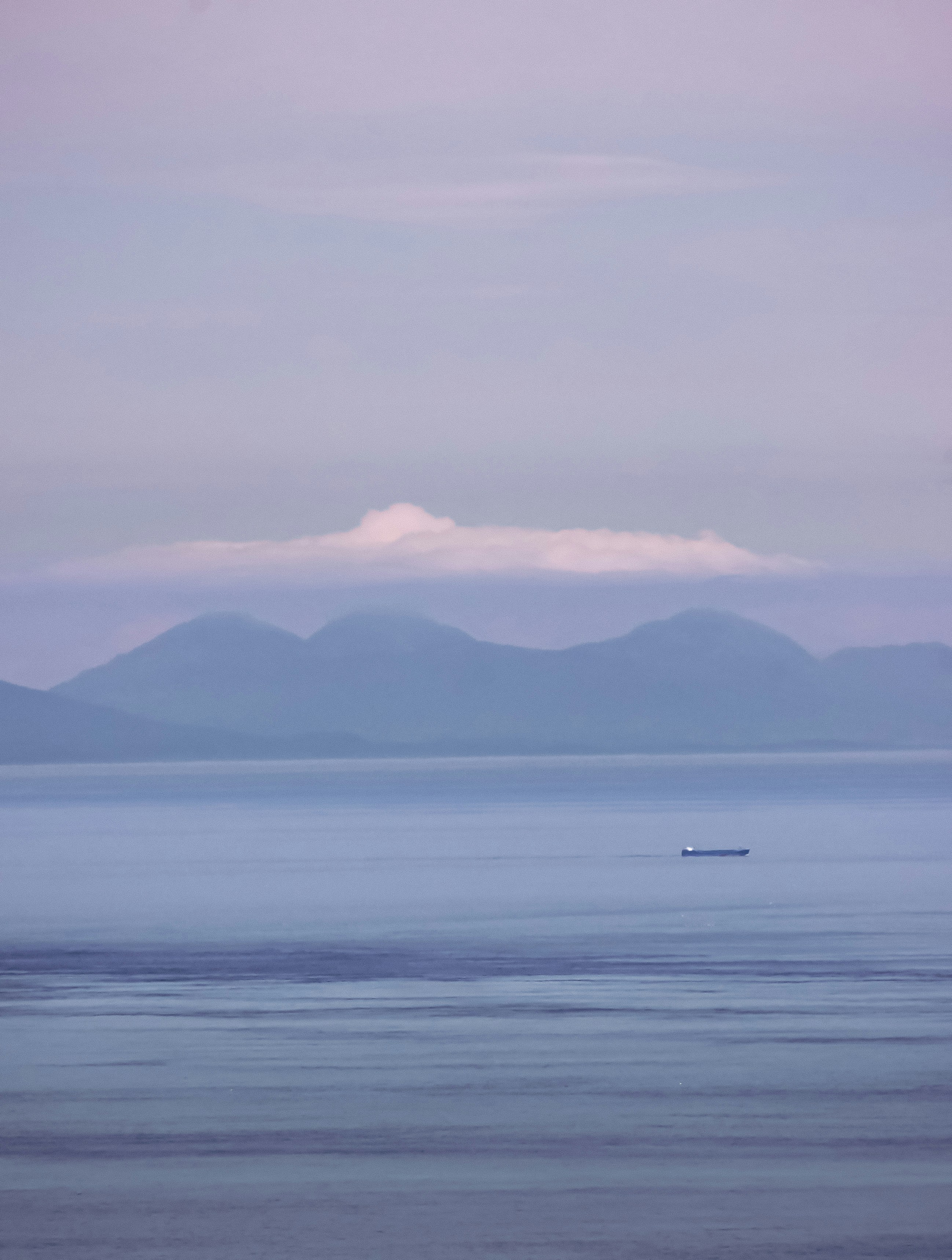 Tanker navigating the tranquil waters near the Scottish Highlands with distant mountains under a pastel sky.