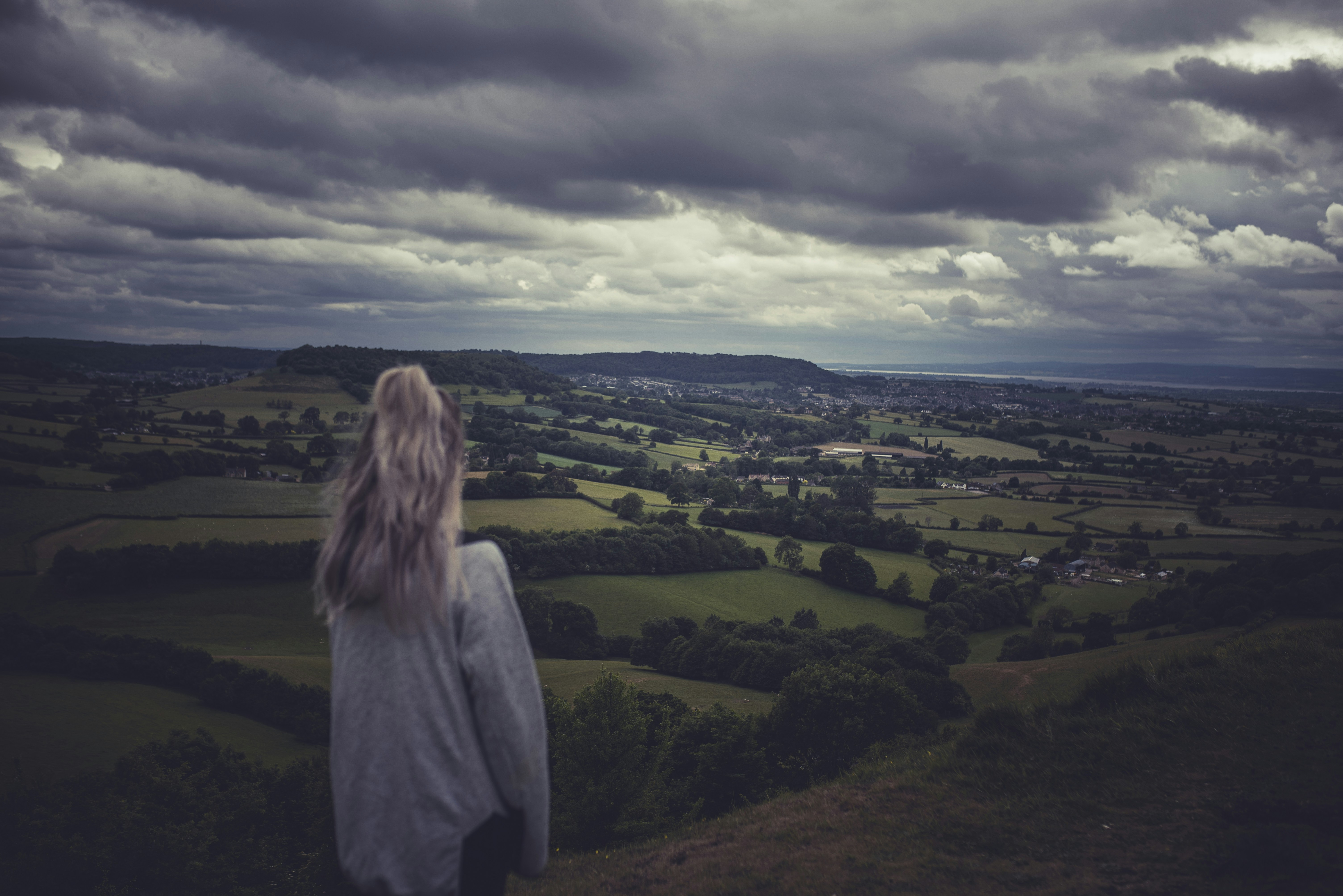Edge of Quiet: A lone figure surveys rolling fields beneath storm-swept skies