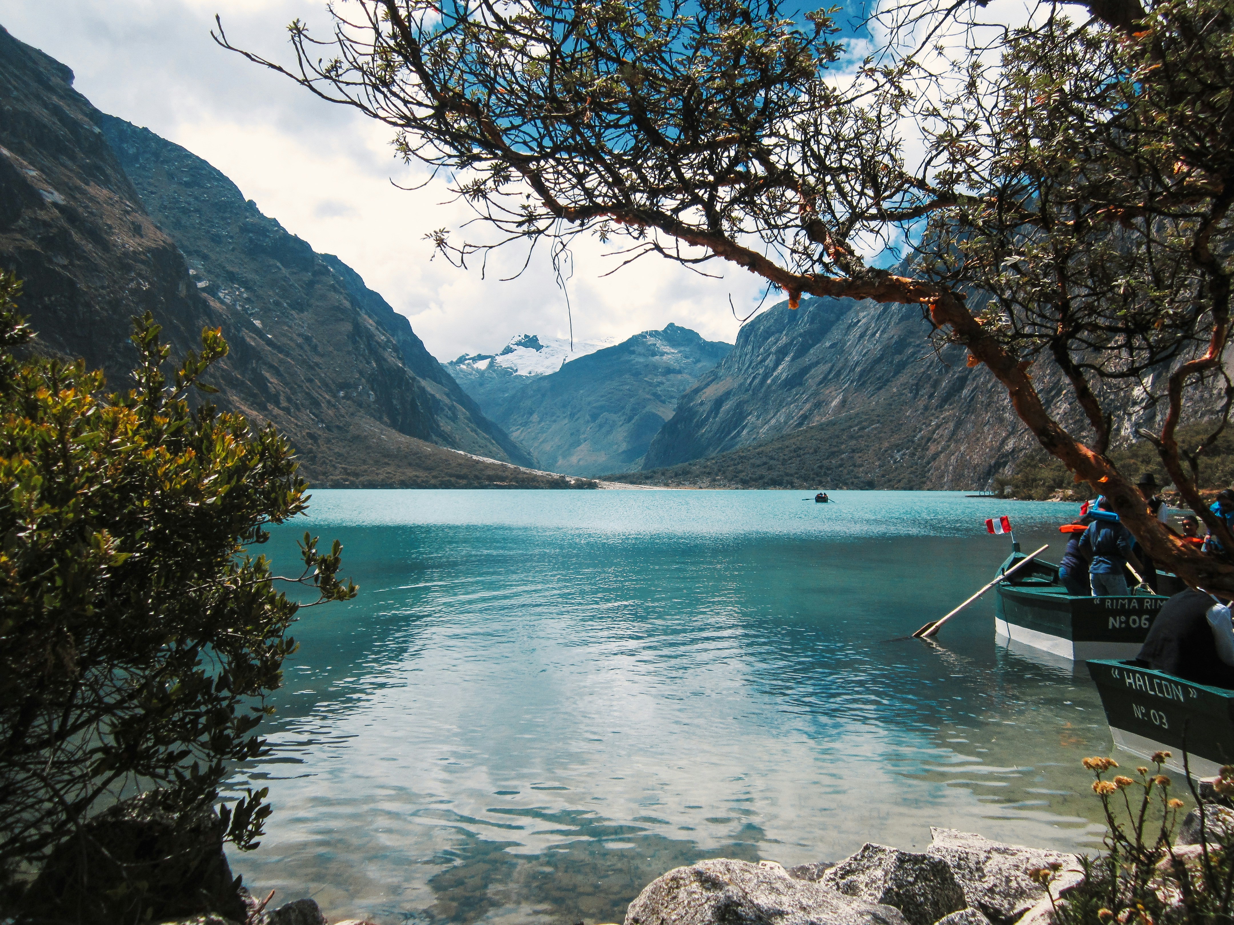 Serene mountain lake surrounded by rugged peaks, with a small boat and overhanging tree branches.