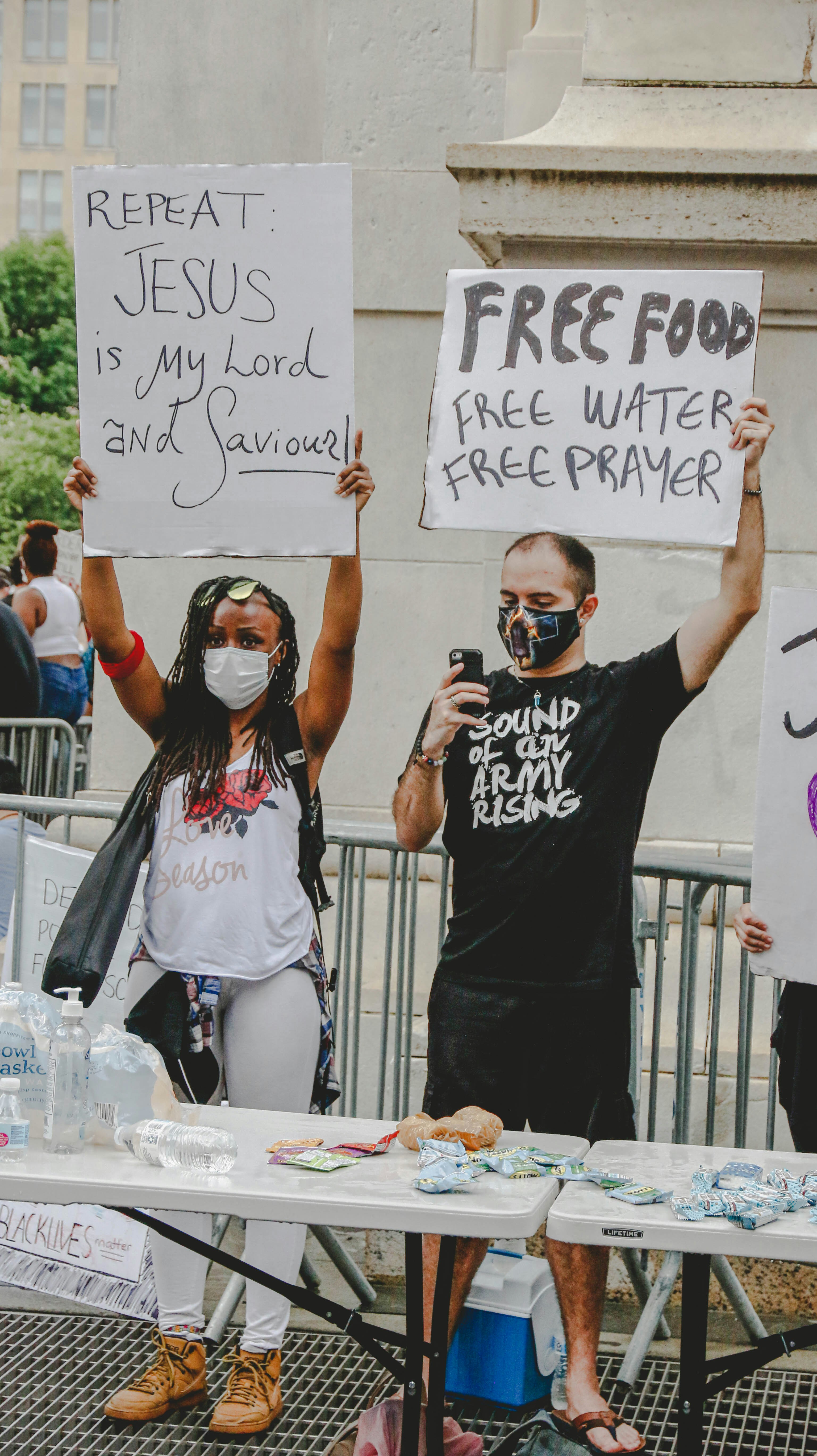 Two Sign-Holders at a City Aid Stand: Free Food, Water, and Prayer
