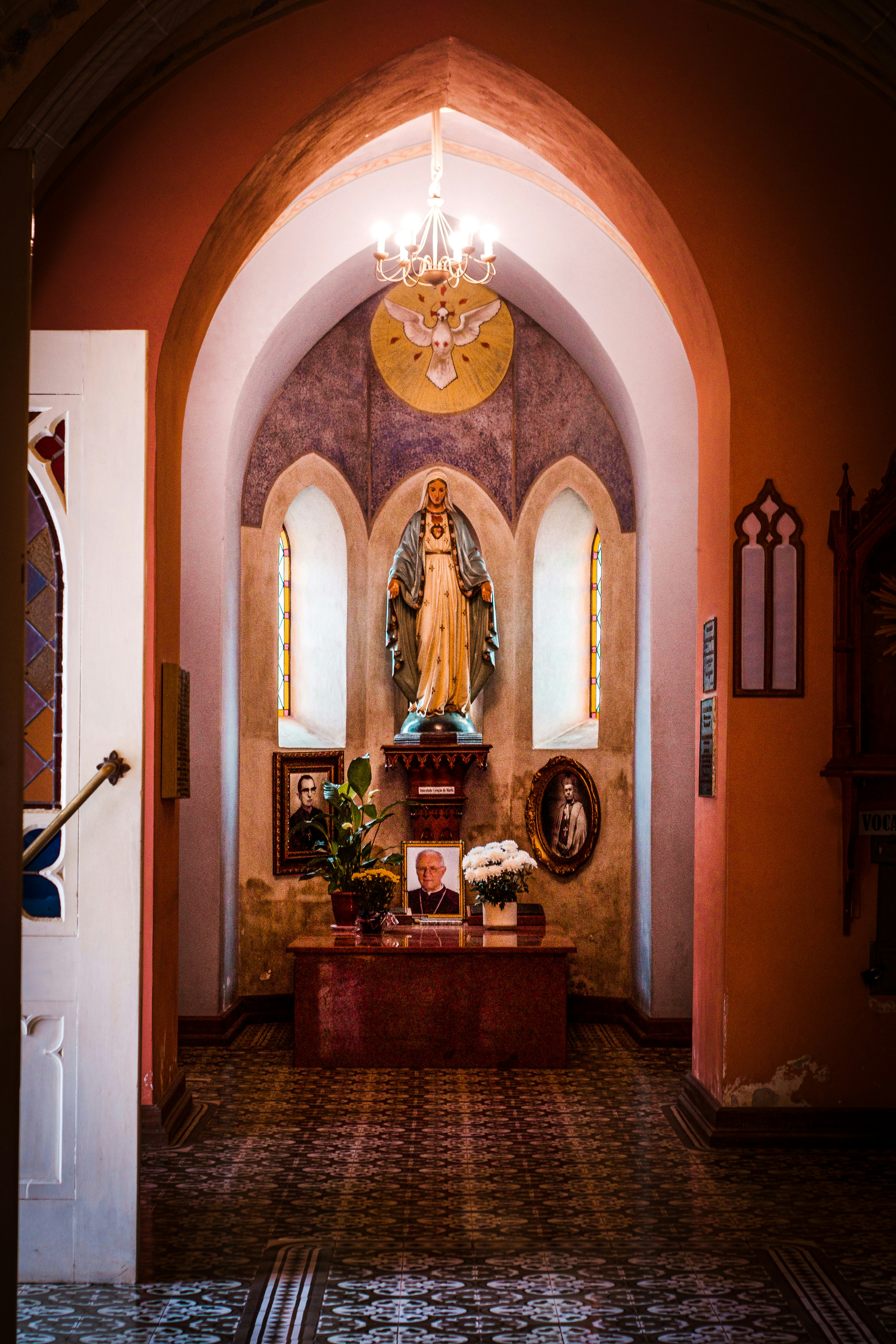 Statue of a religious figure in a softly lit alcove with arched architecture and patterned floor tiles.