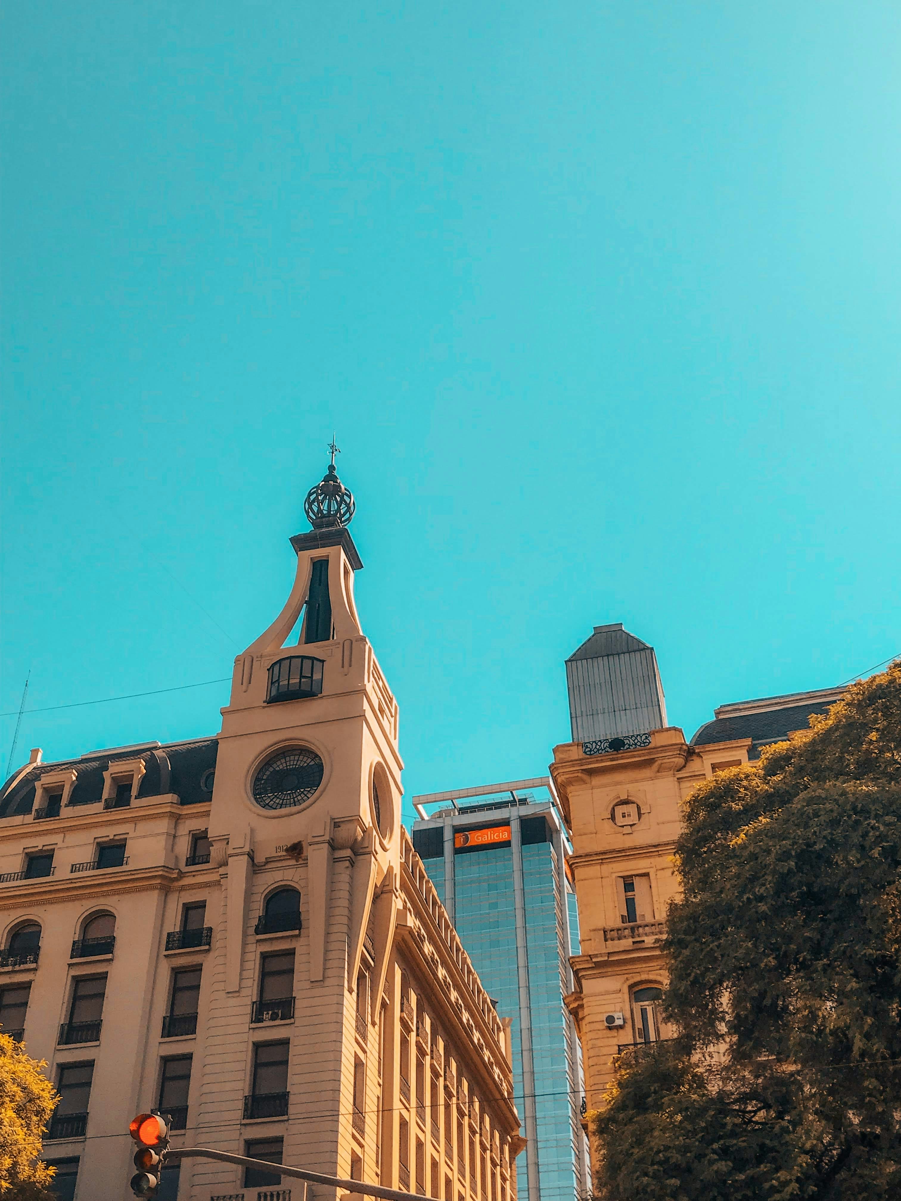 Historic building with ornate clock tower juxtaposed against sleek modern skyscraper under a clear blue sky.