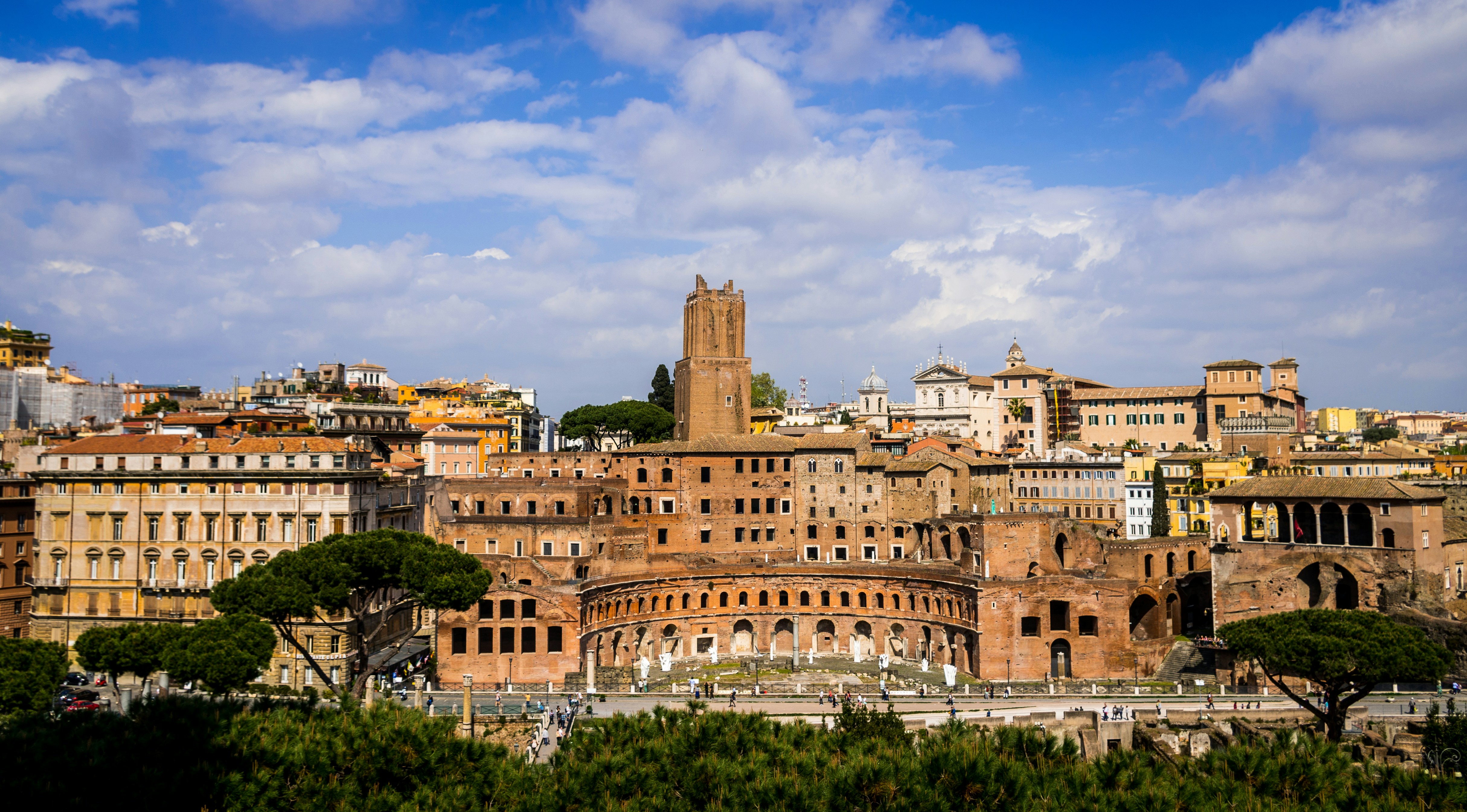 The majestic ruins of the Roman Forum rise against a backdrop of vibrant city life, showcasing a blend of history and modernity. The scene captures the timeless essence of Rome's architectural heritage.