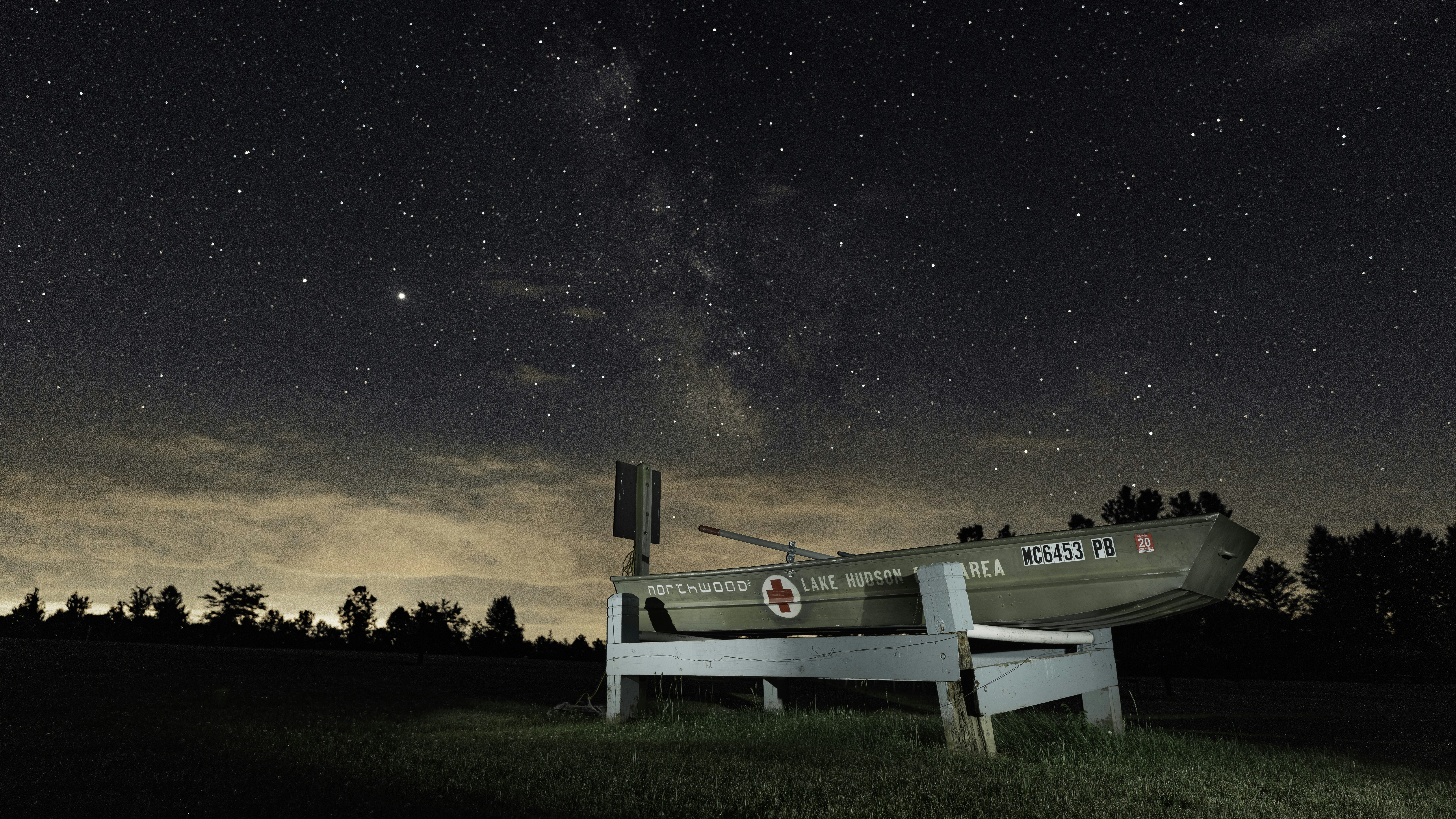 Wooden boat resting on grass beneath a star-filled night sky.