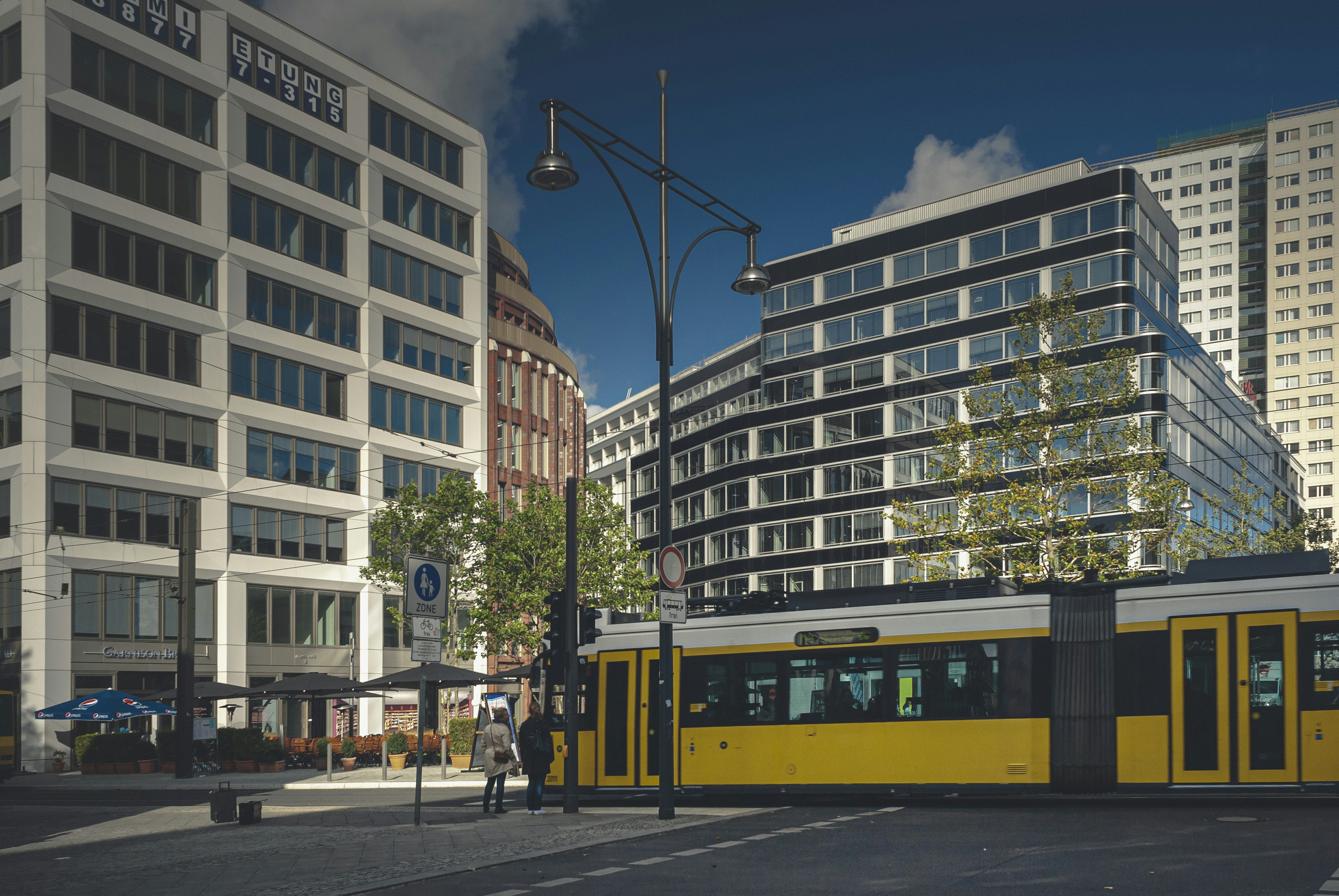 A vibrant yellow tram glides past modern buildings, showcasing the interplay of urban architecture and public transport.