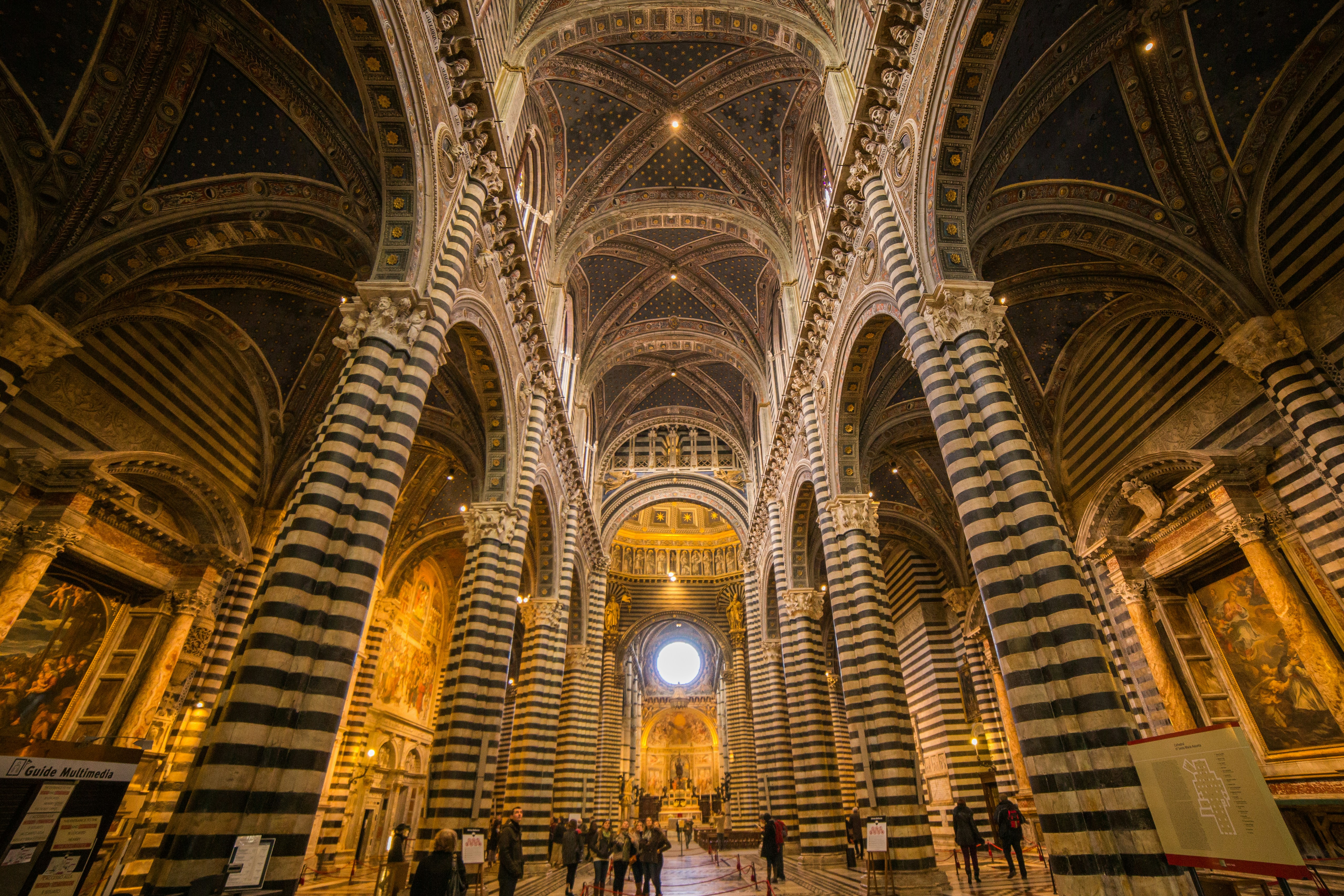 Interior of a grand cathedral featuring striking striped columns and an ornate ceiling, with visitors admiring the architectural beauty.