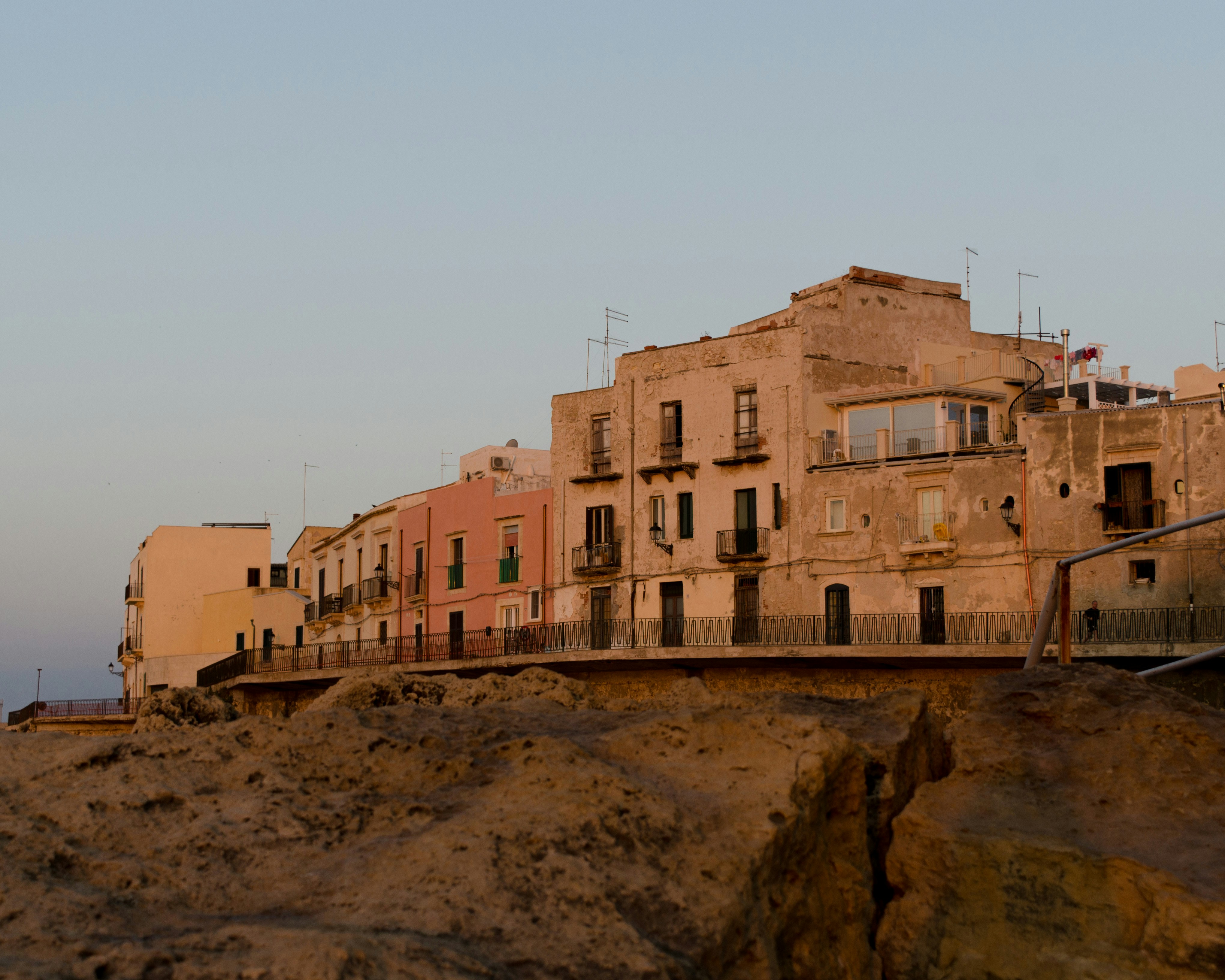 Row of rustic buildings on a rocky cliff under a clear blue sky.