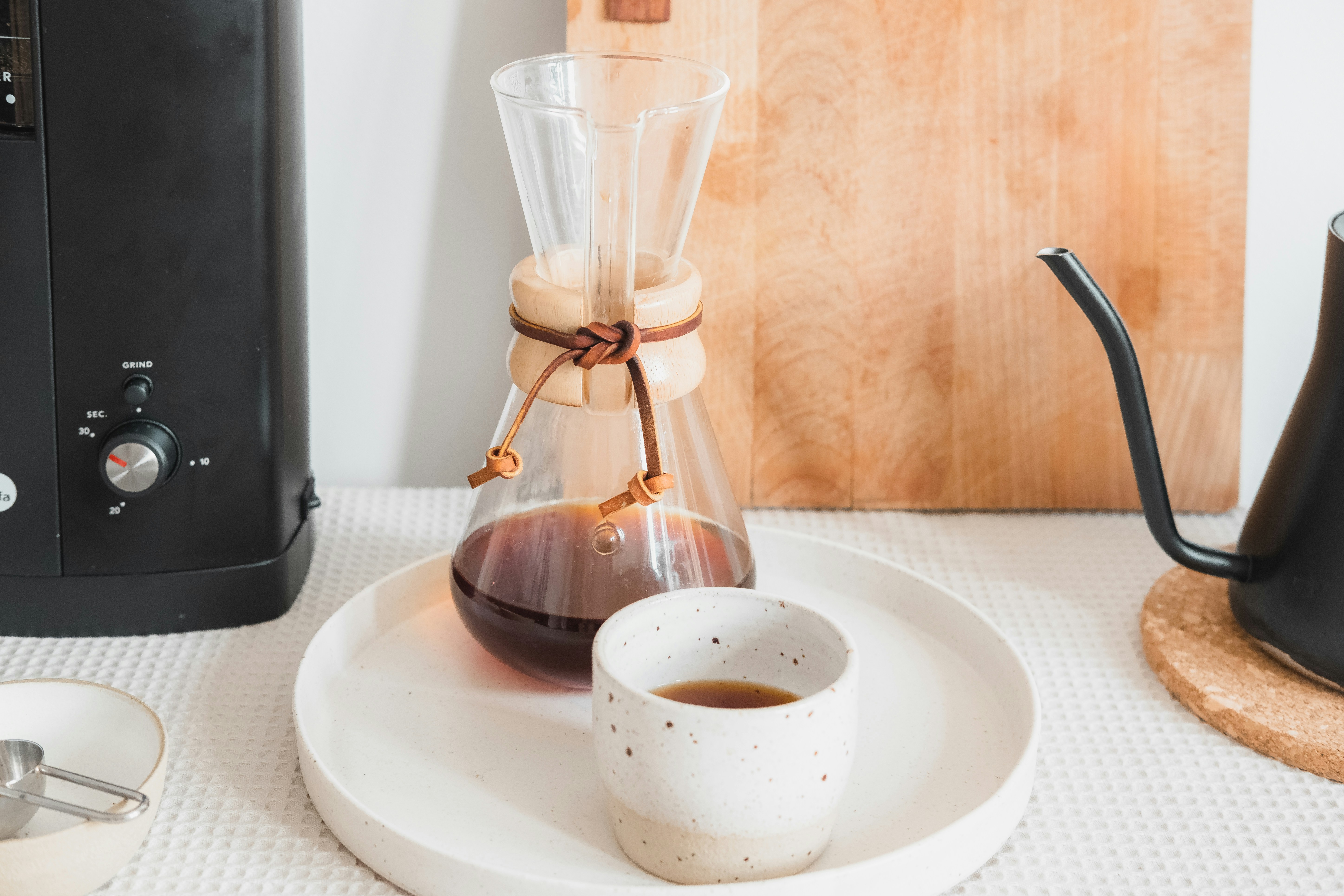 Chemex coffee maker with brewed coffee and a ceramic cup on a minimalist tray in a bright kitchen setting.