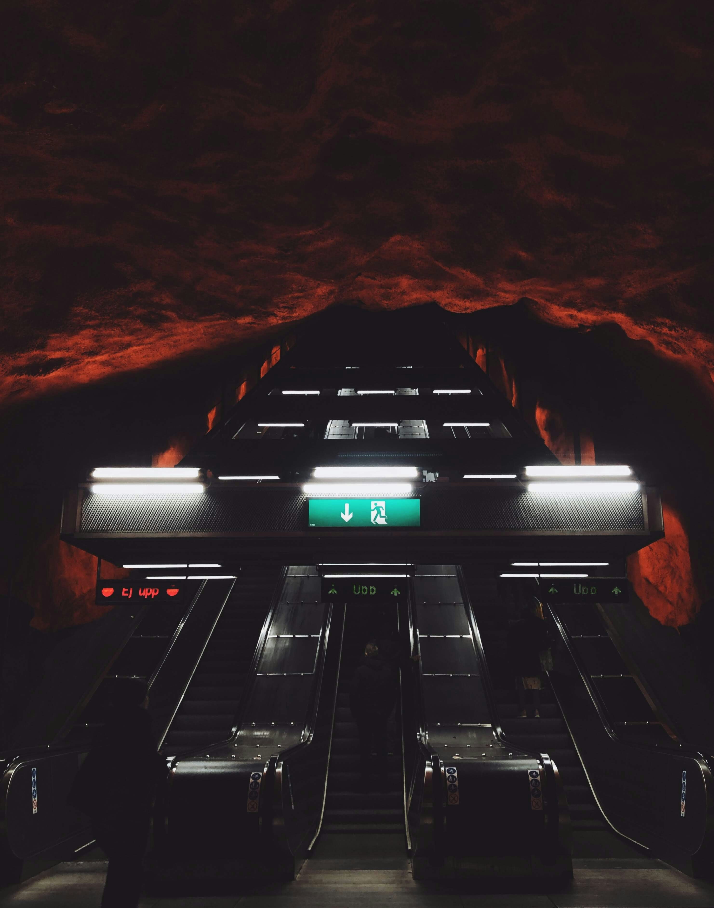 Emerald Exit in a Lava-lit Cavern: Escalators Descend into Red Rock
