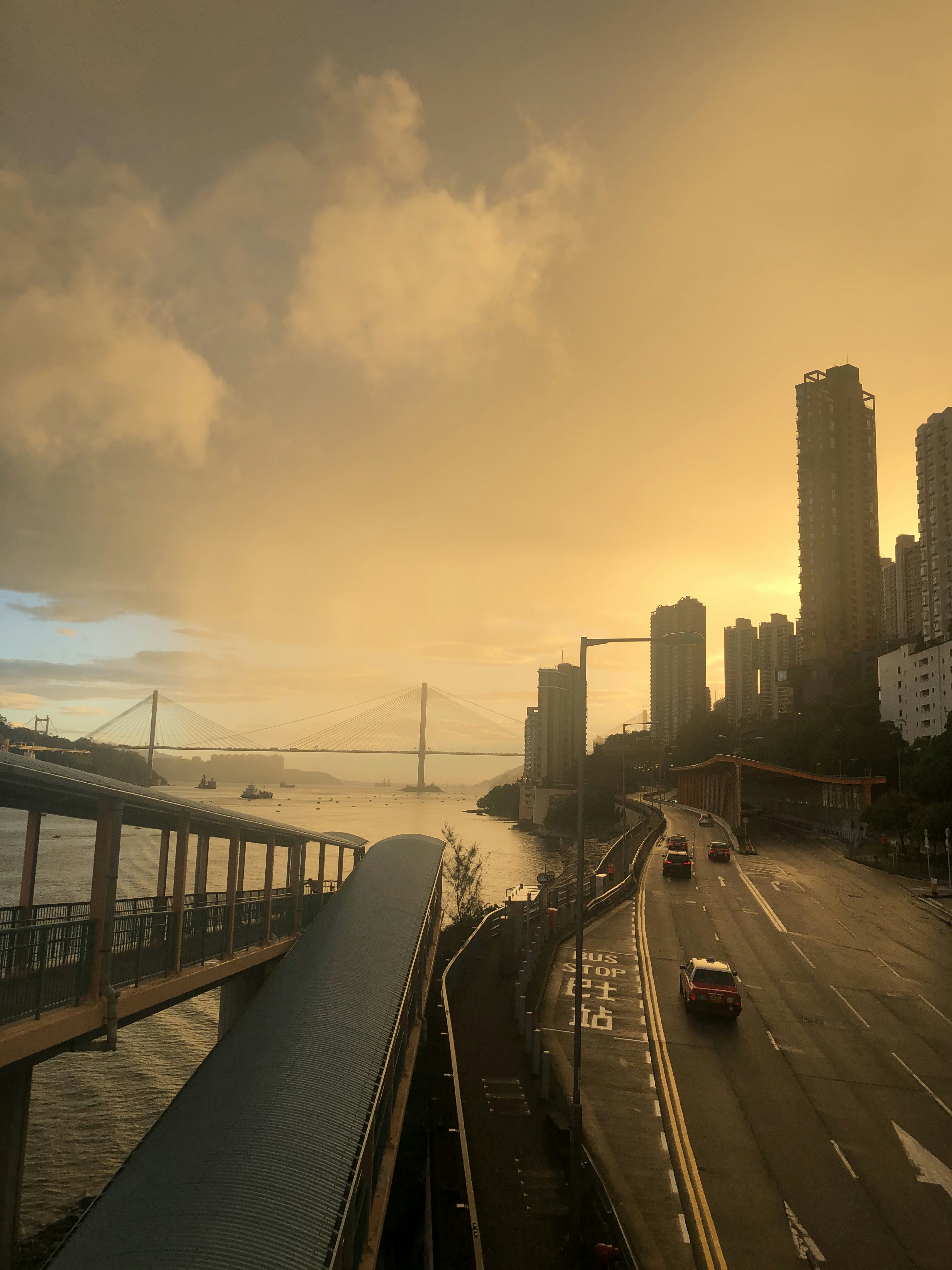 Golden hues illuminate the skyline as a bridge spans the river, with urban buildings towering in the background. The scene captures the transition from day to night.