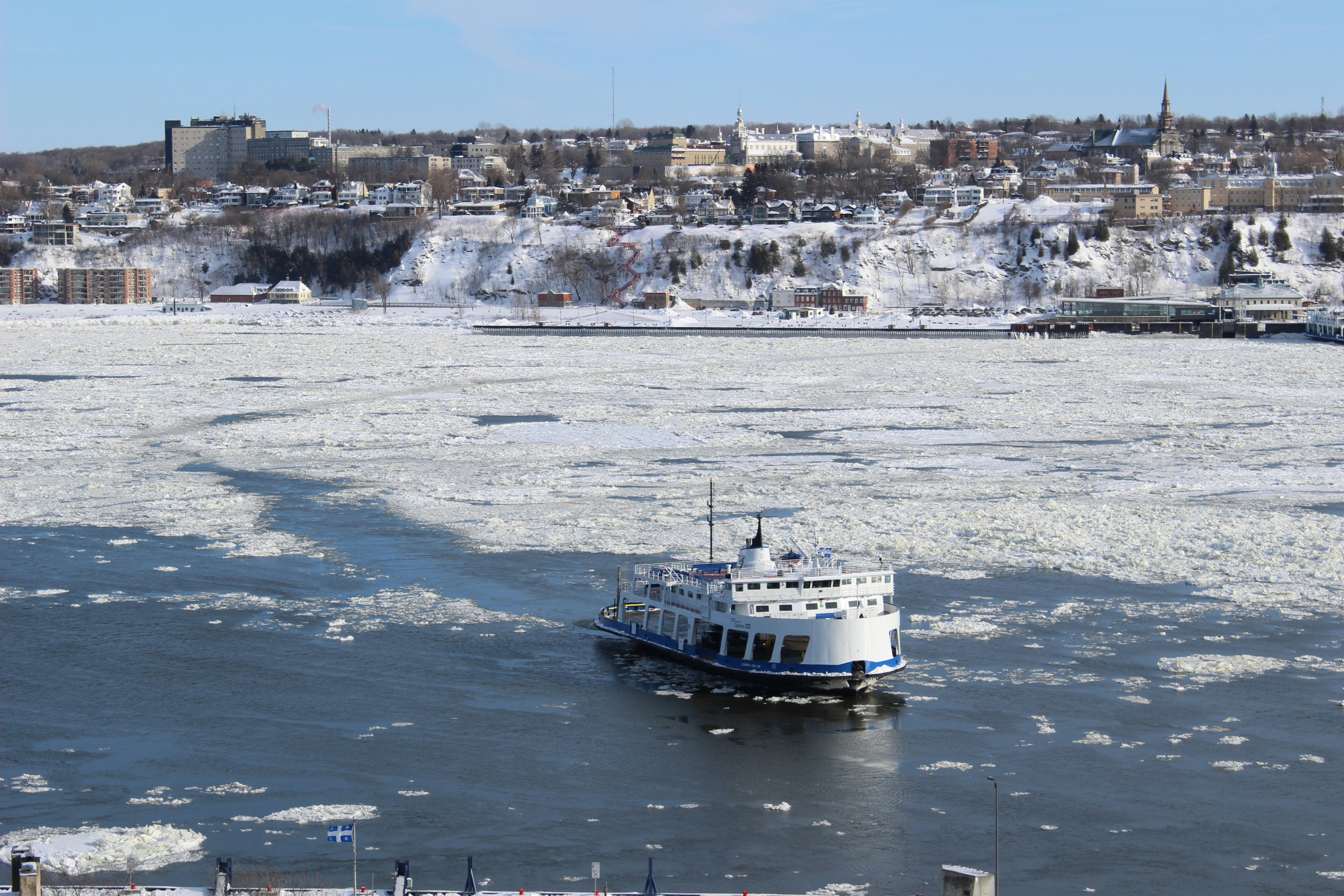 Ferry navigating through ice-laden waters with a snowy cityscape in the background.