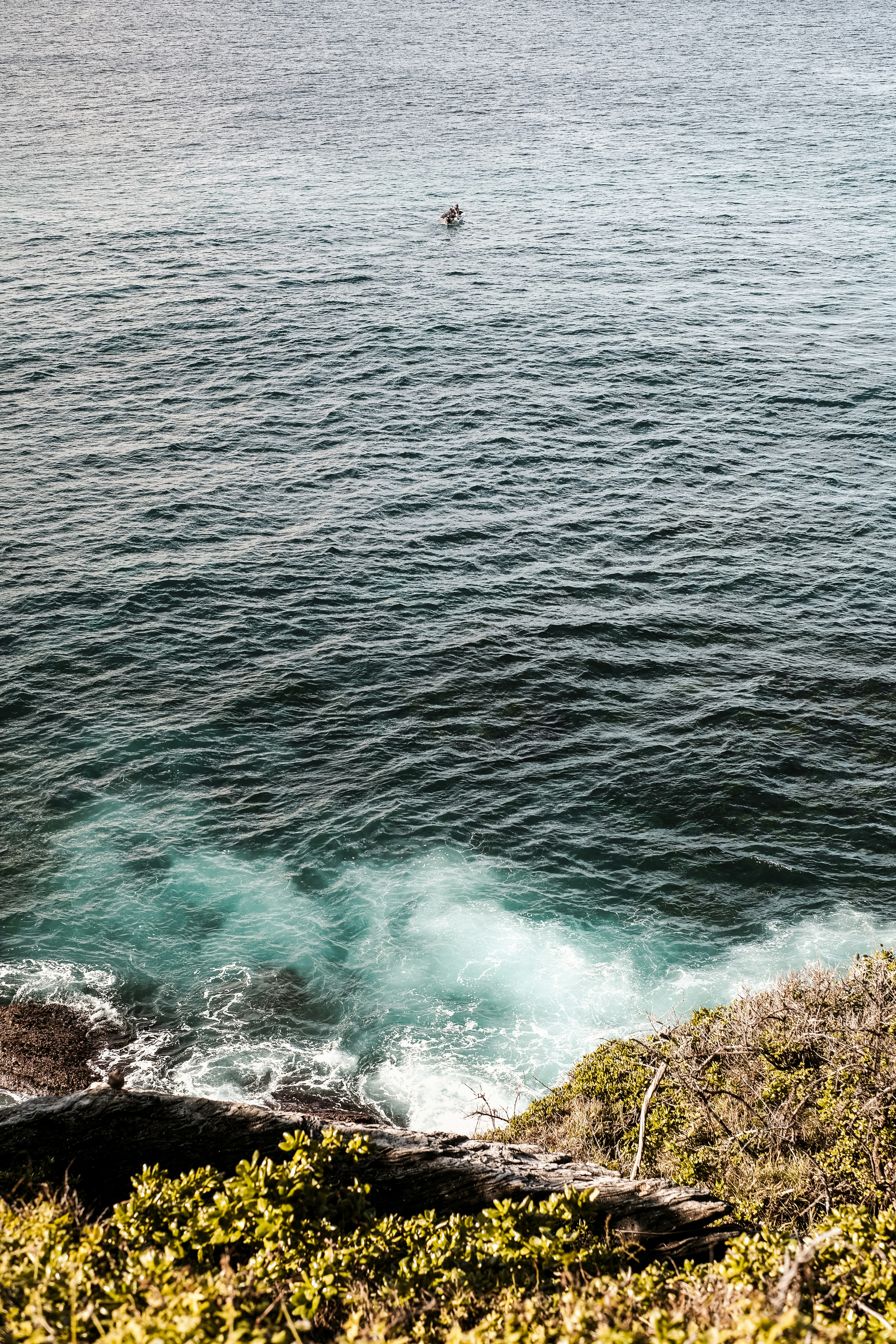 Horizon Vessel: A Tiny Craft on Turquoise Breakers from a Cliffside Verge