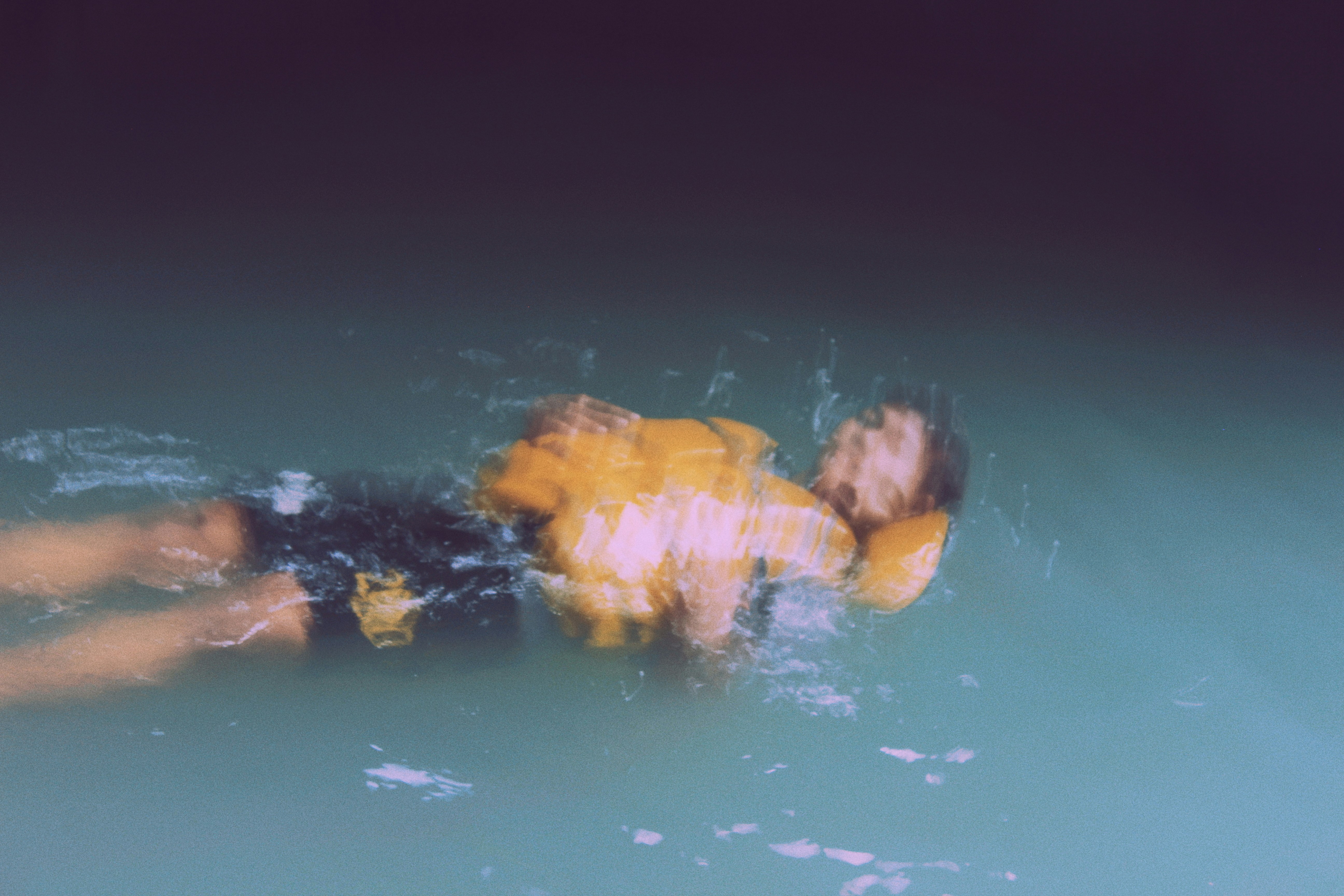Person in an orange life jacket floating calmly on turquoise water, creating a serene and blurred motion effect.