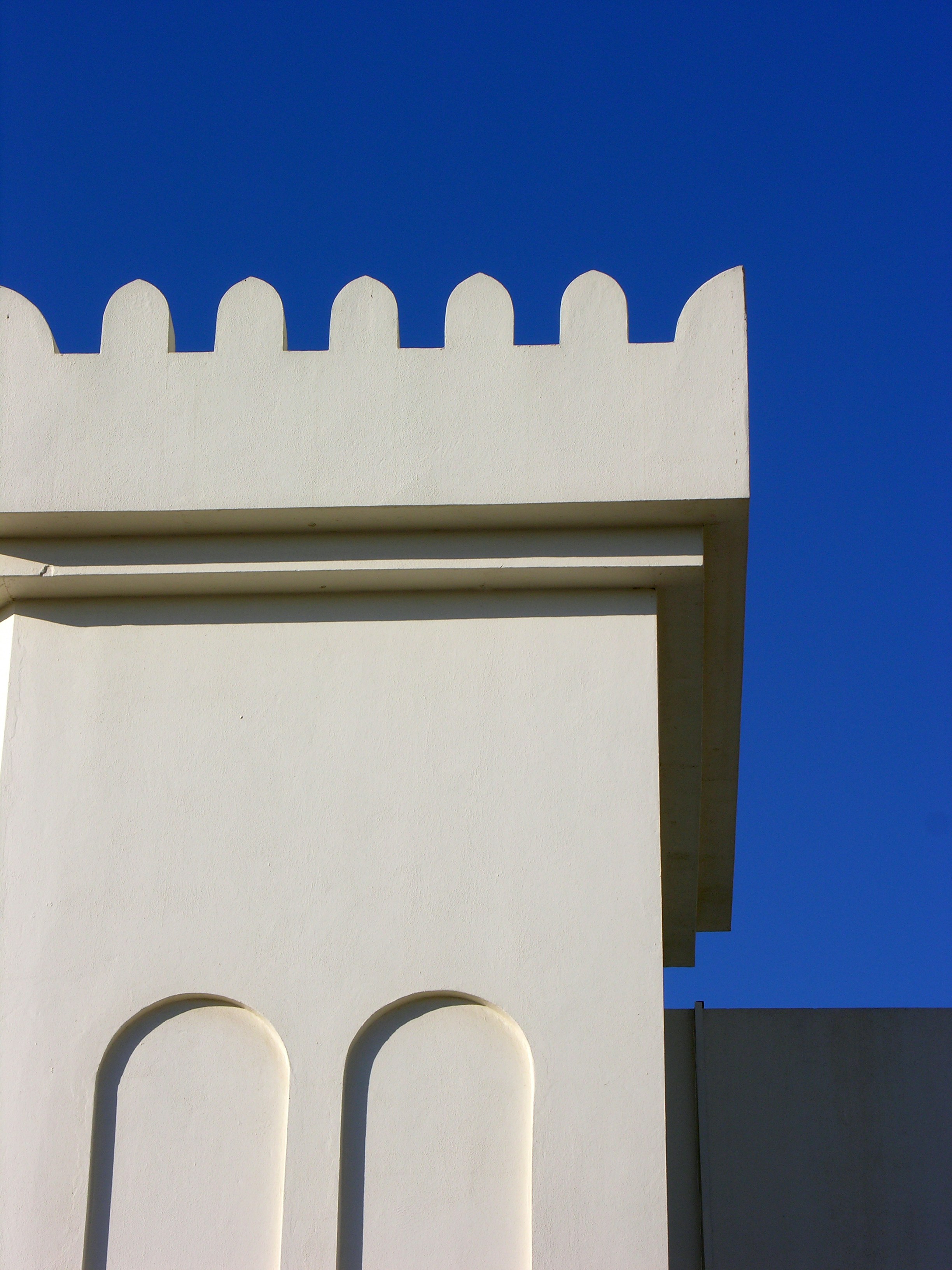White stucco architecture with a scalloped parapet rises against a vivid blue sky.