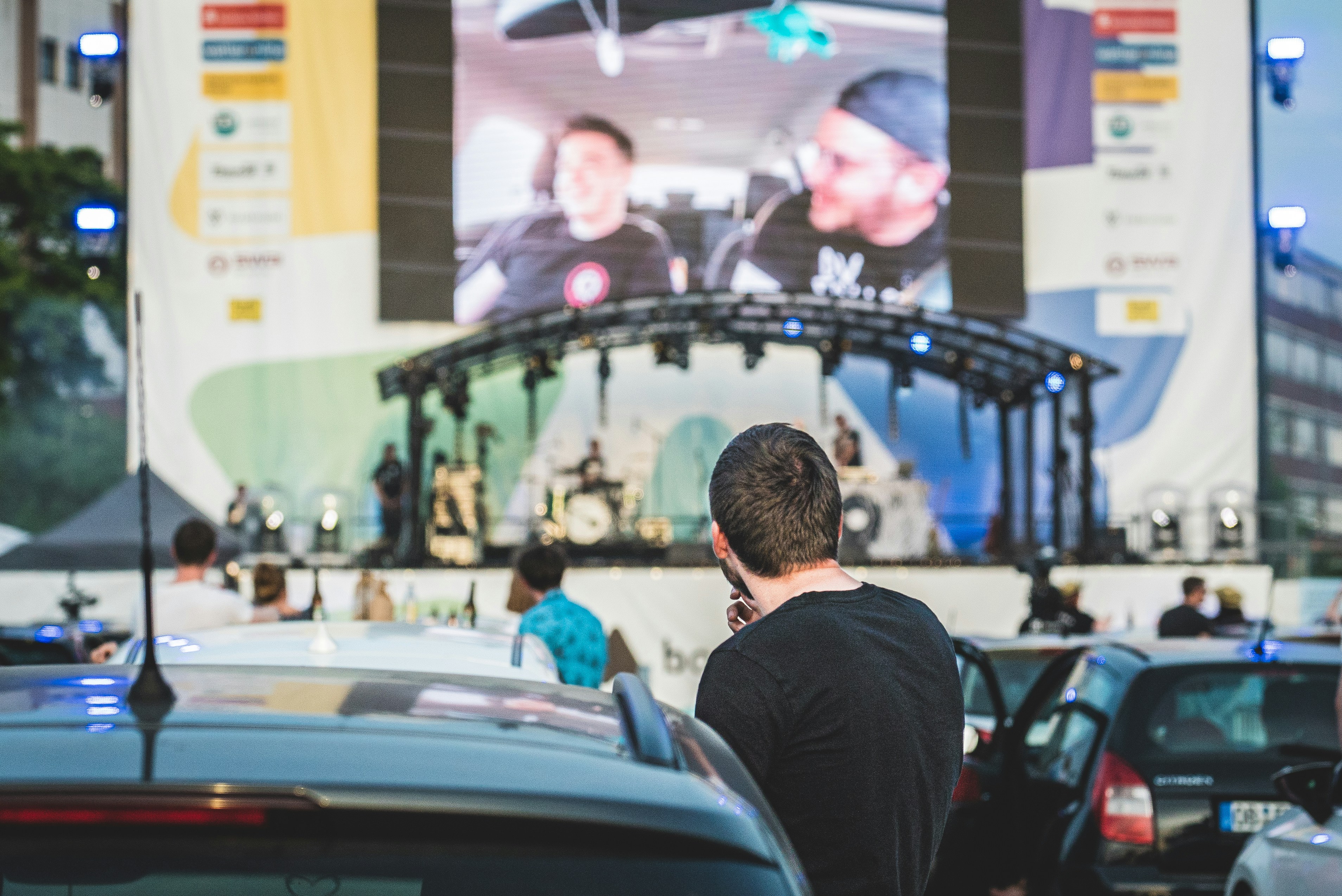 Parking Lot Audience: A Man Watches a Live Outdoor Show as Cars Frame the Scene