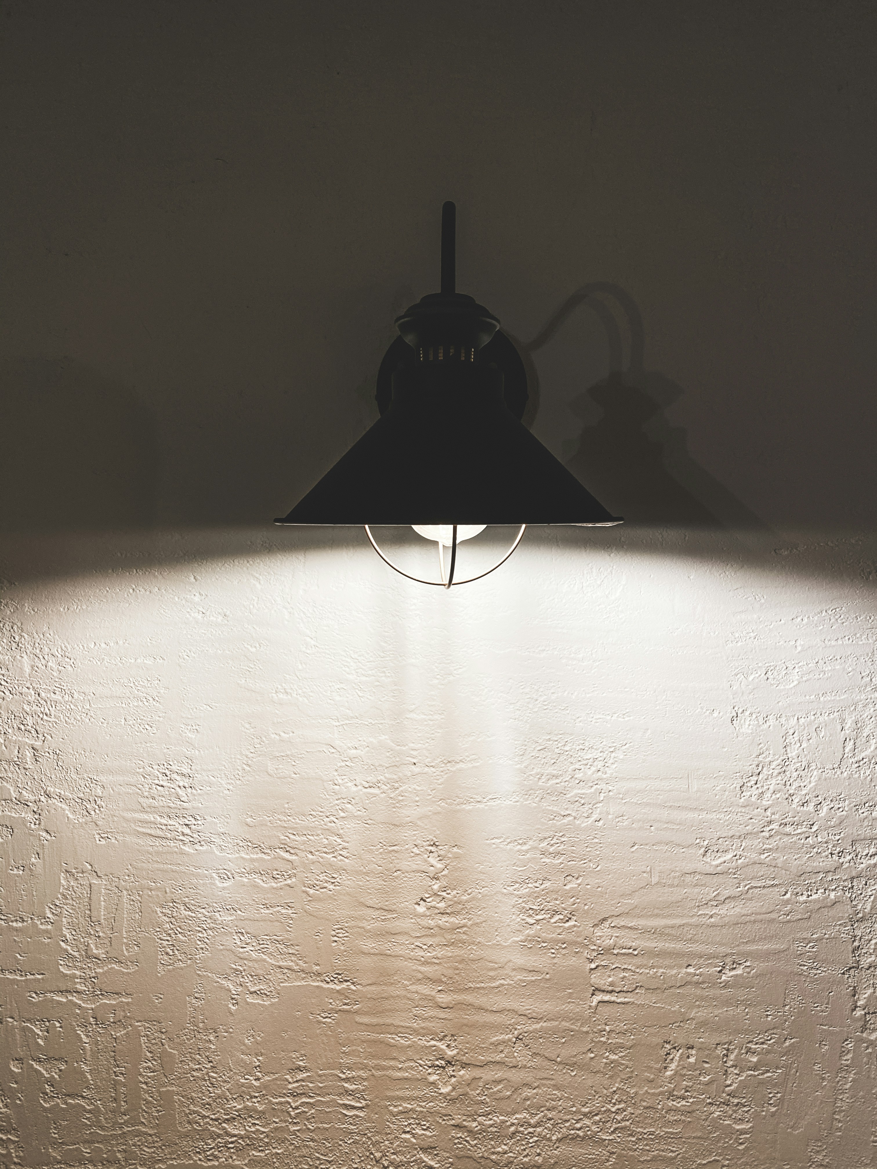 A sleek black lamp casts a warm glow against a textured white wall, creating a striking contrast of light and shadow.