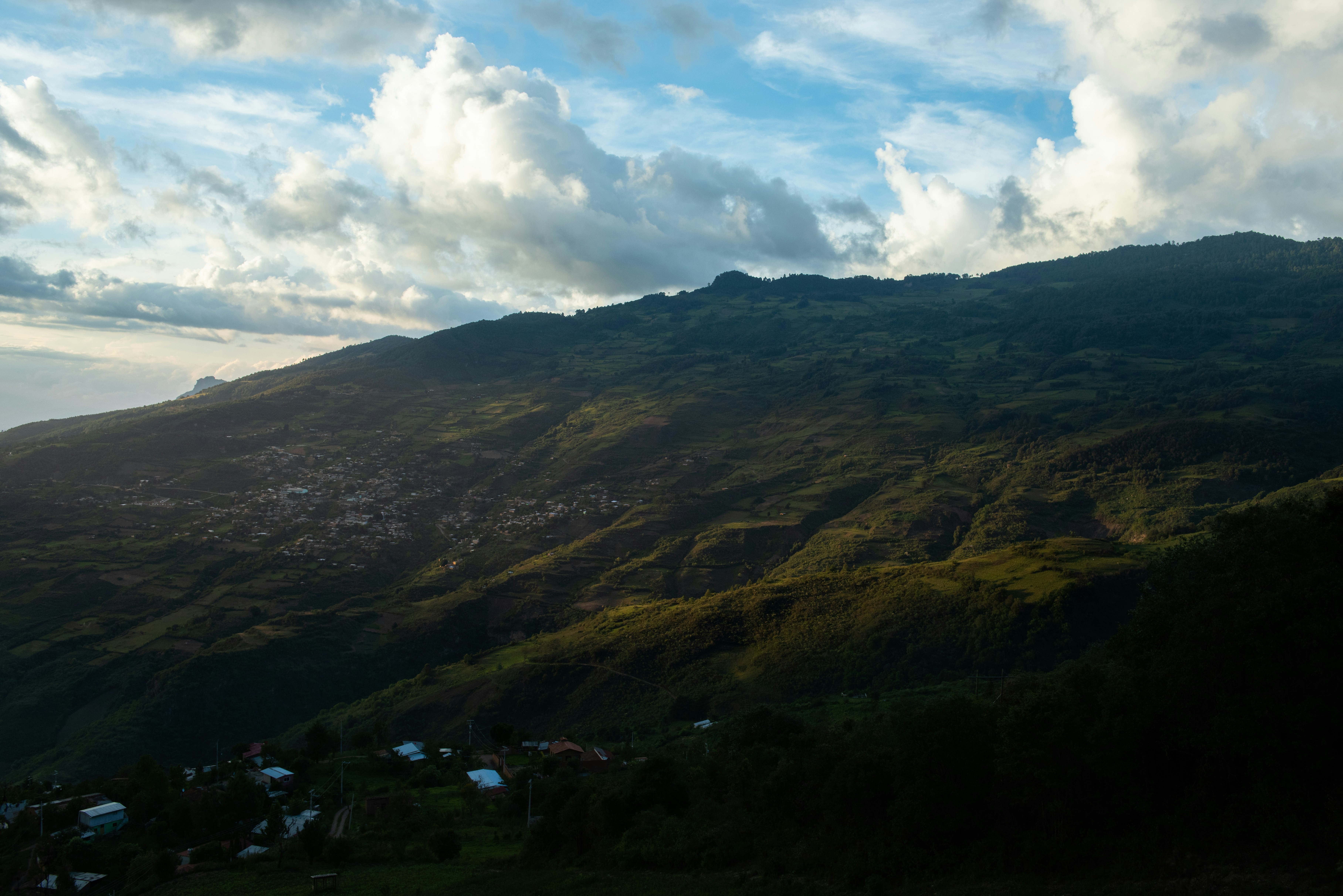 Rolling green hills beneath a dramatic sky with scattered clouds in the Oaxaca mountain range.