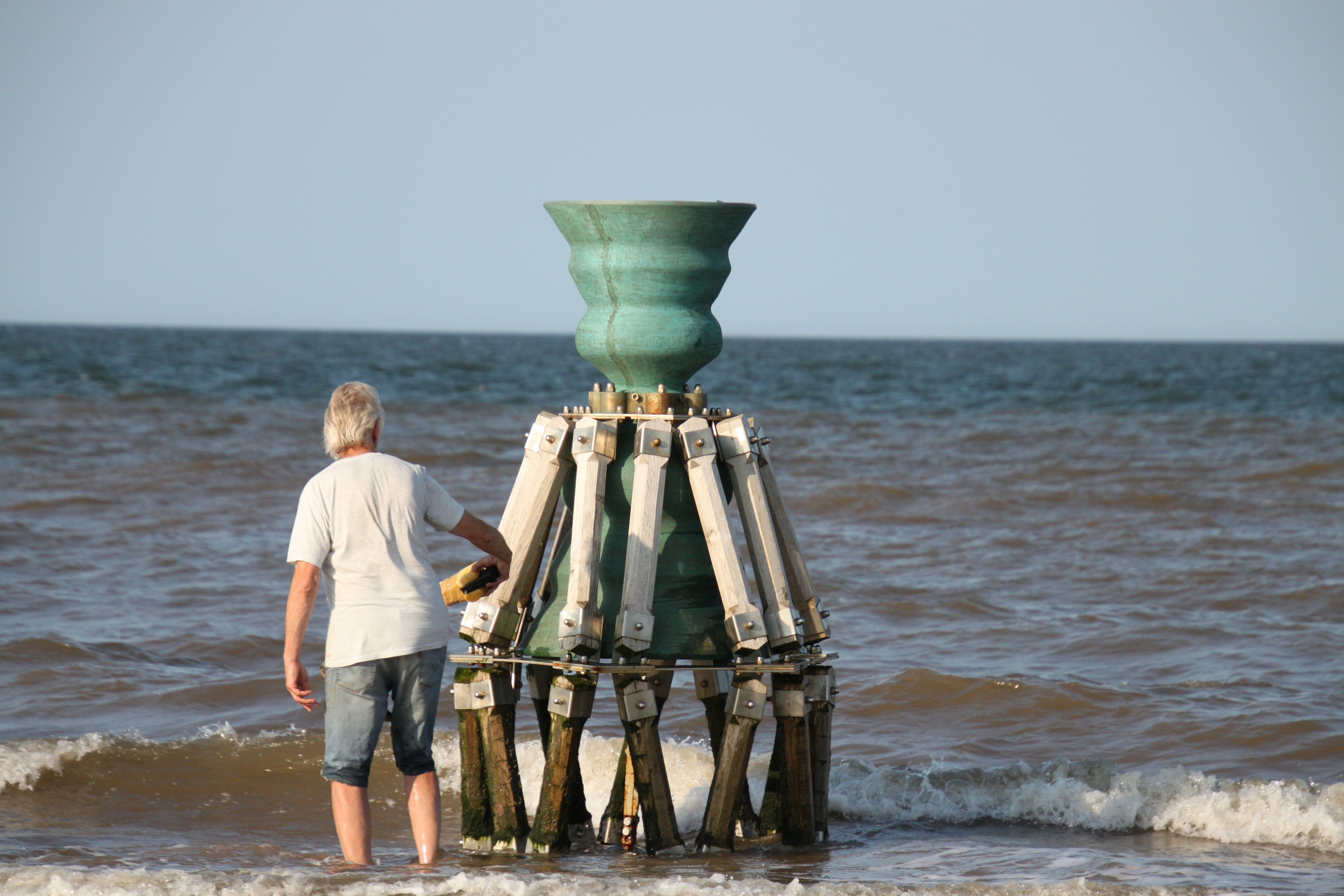 Shoreline Sentinel: A Weathered Green Funnel Rising on Wooden Stilts