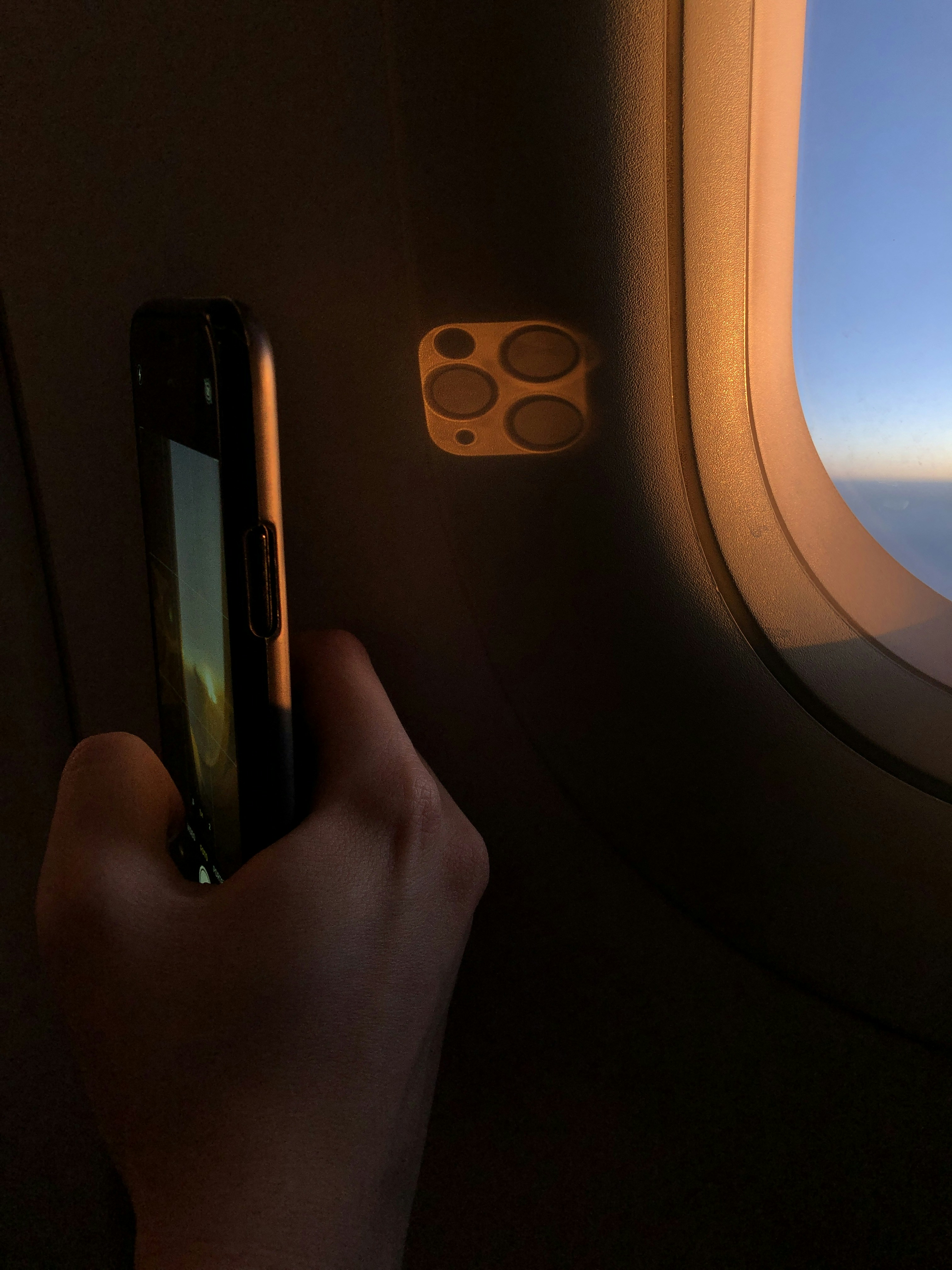 A hand holding a smartphone takes a photo of a sunset from an airplane window, highlighting the blend of technology and nature's beauty.