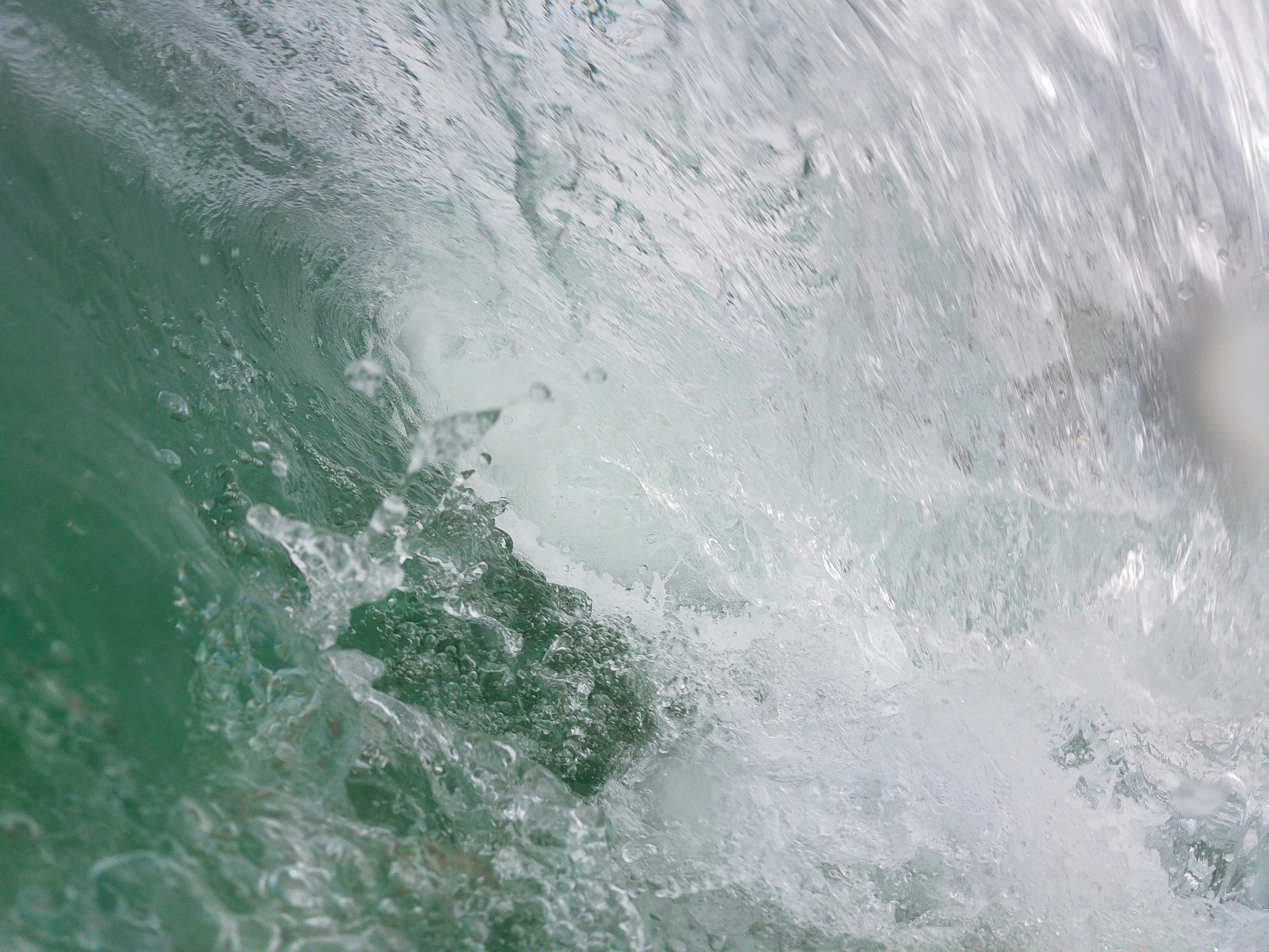 Close-up of a breaking green wave with white foam and spray, viewed from within the curl for a dynamic underwater perspective.