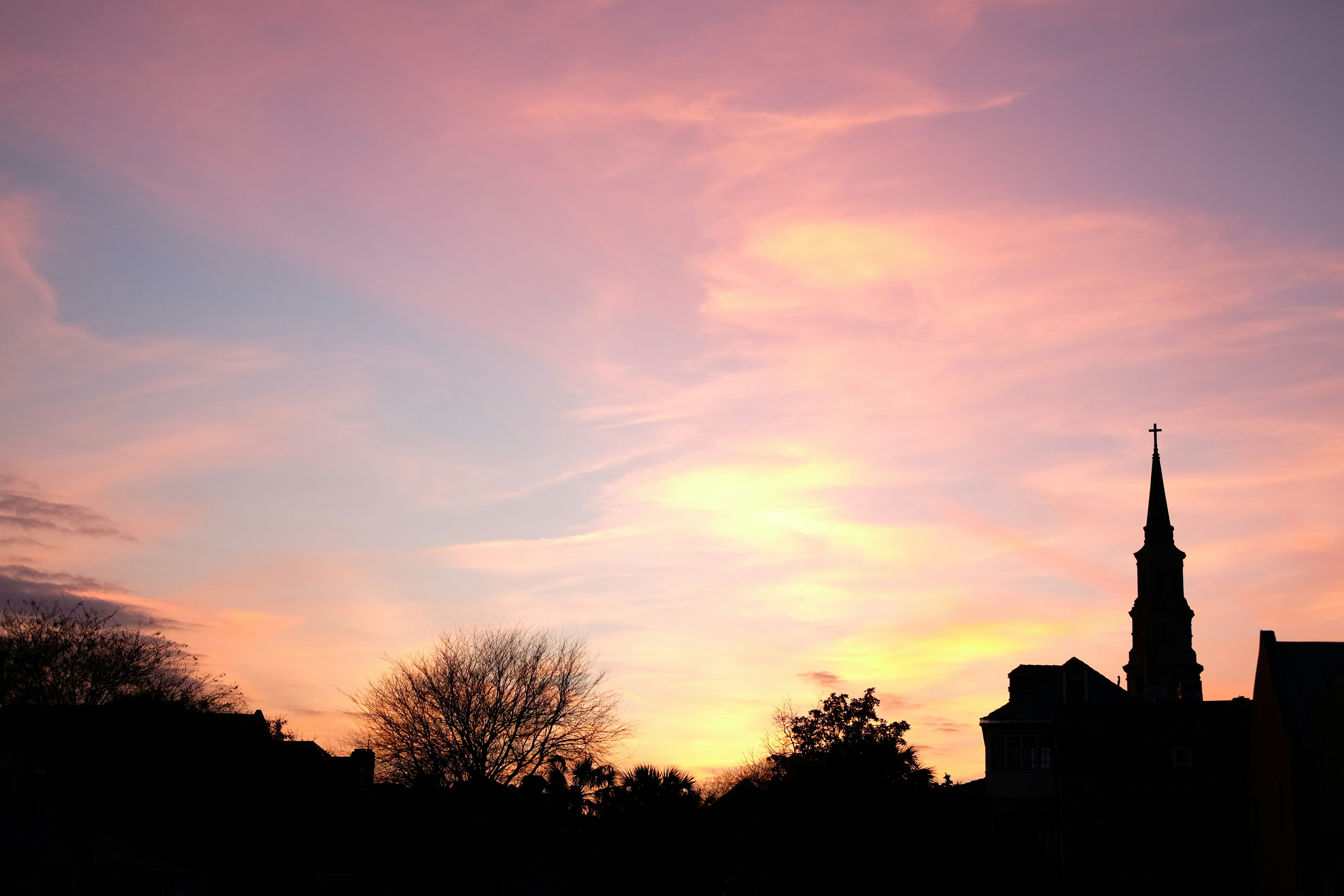 Silhouette of trees and a church steeple against a vibrant sunset sky with pink and orange hues.