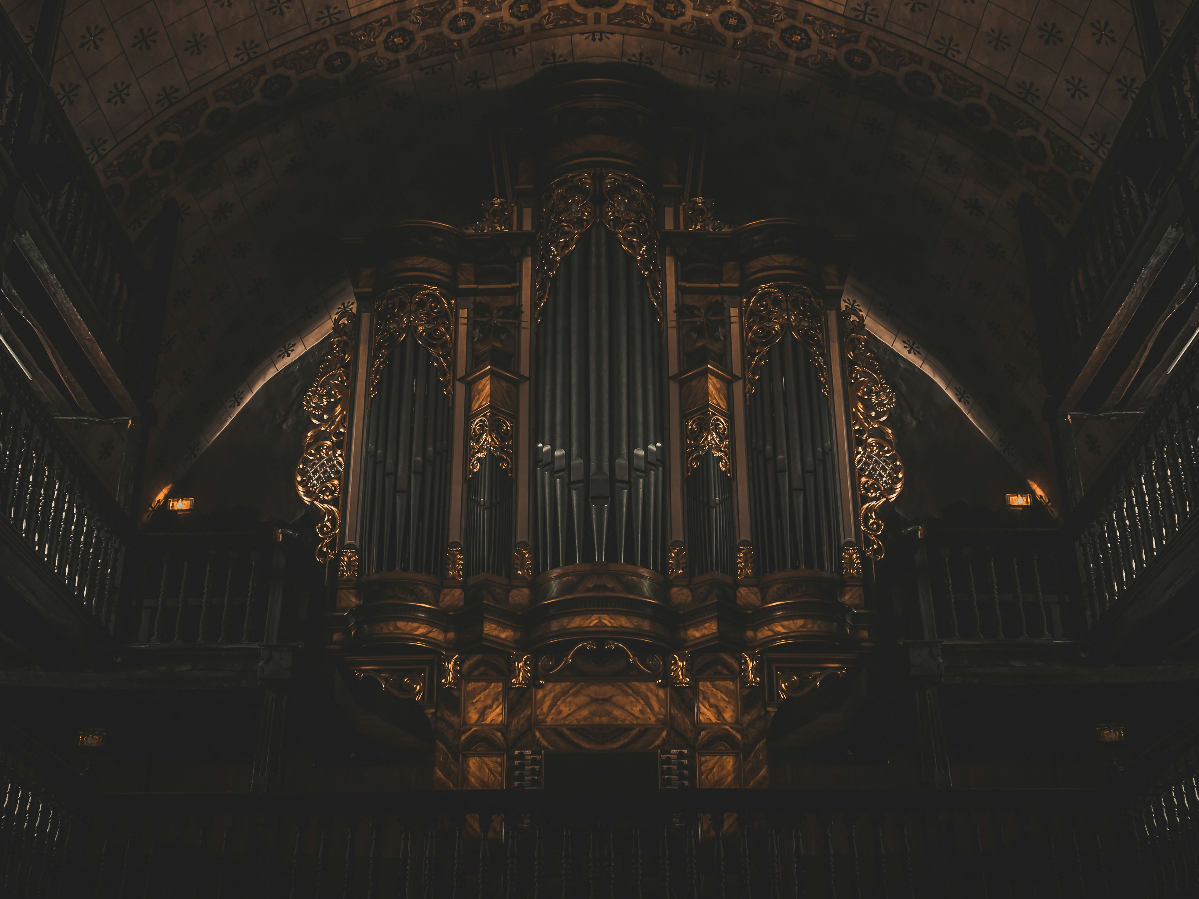 Intricately carved wooden organ with golden accents under an ornate arched ceiling.