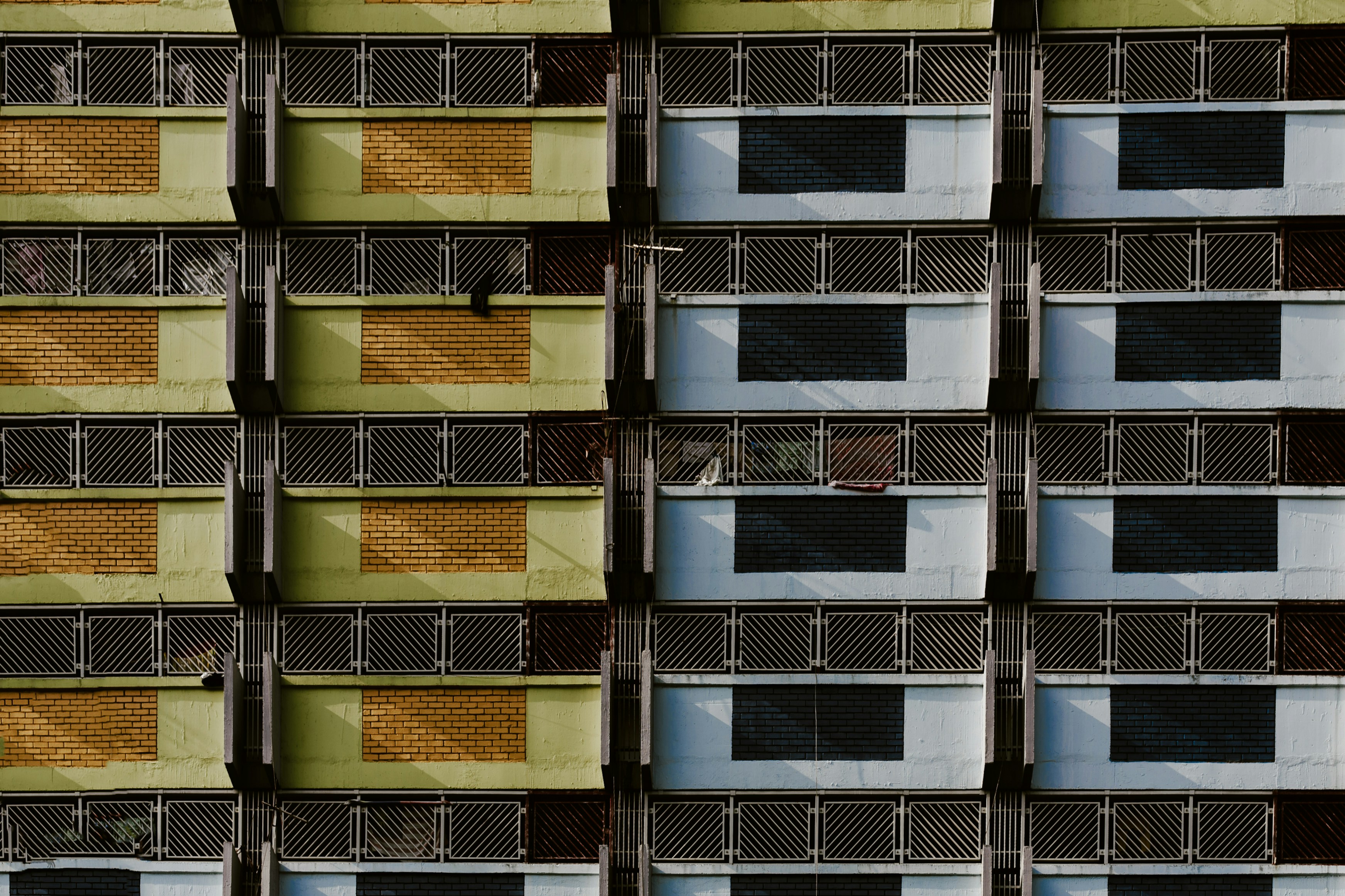 Facade of a building with alternating green and blue panels, featuring consistent geometric shapes.