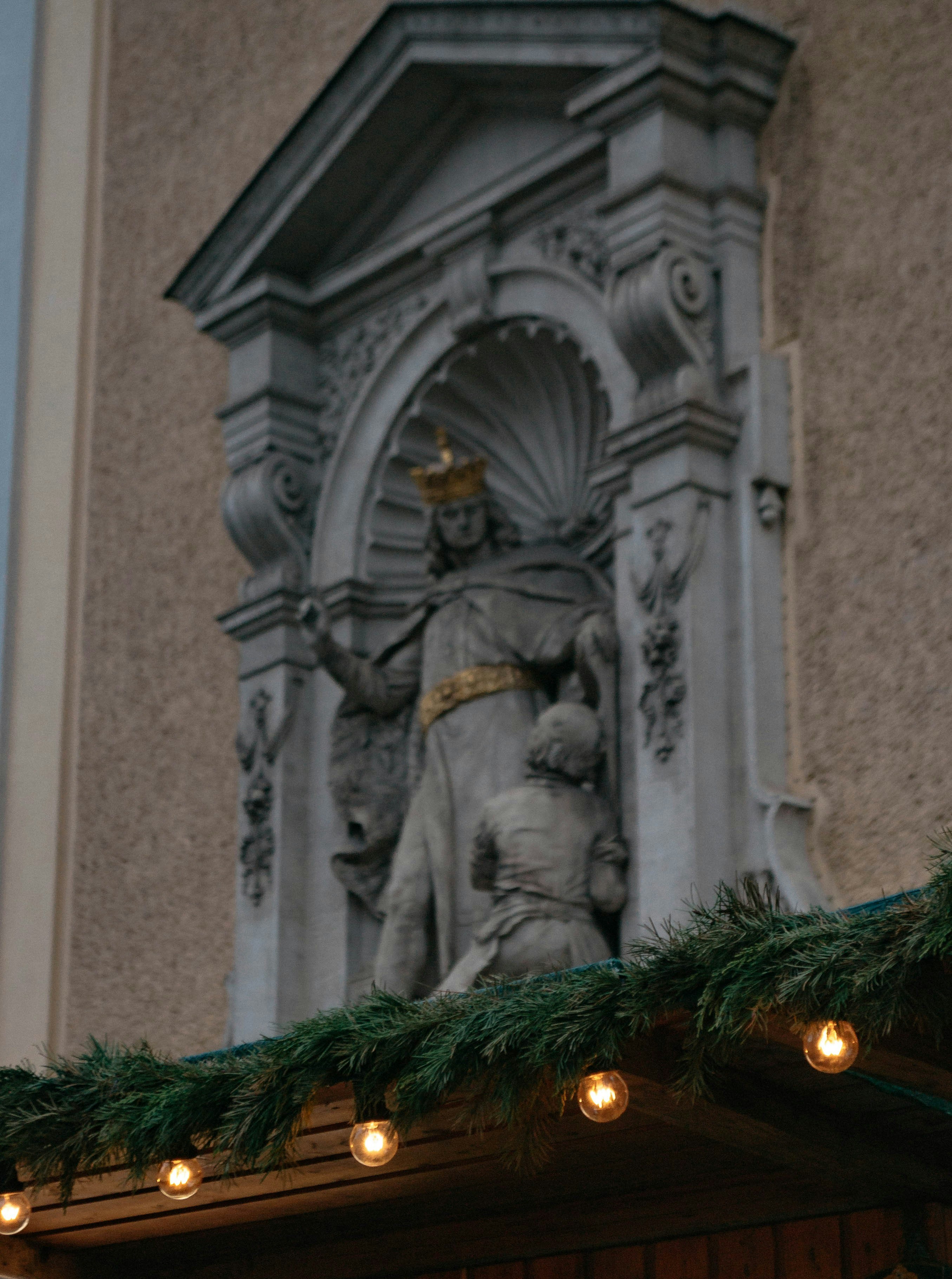 Detailed stone statue of a crowned figure interacting with a child, adorned with holiday decorations. The scene captures the essence of festive spirit.