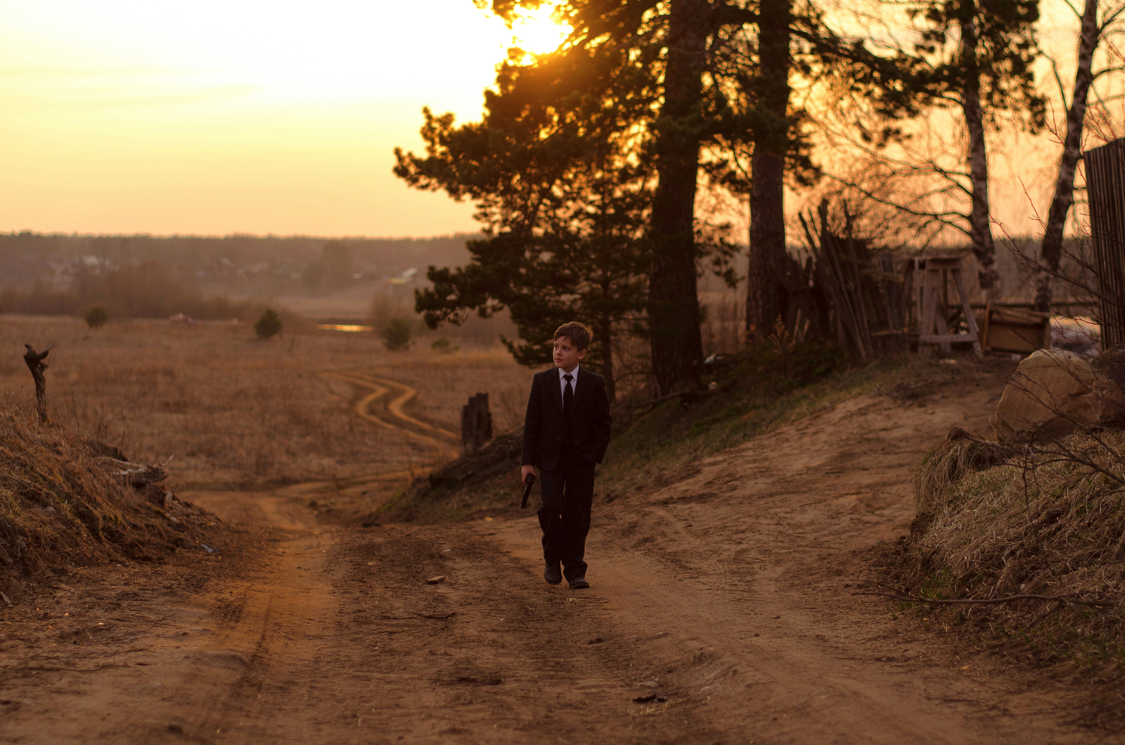 Child walking down a dirt path at sunset, framed by trees and open fields.