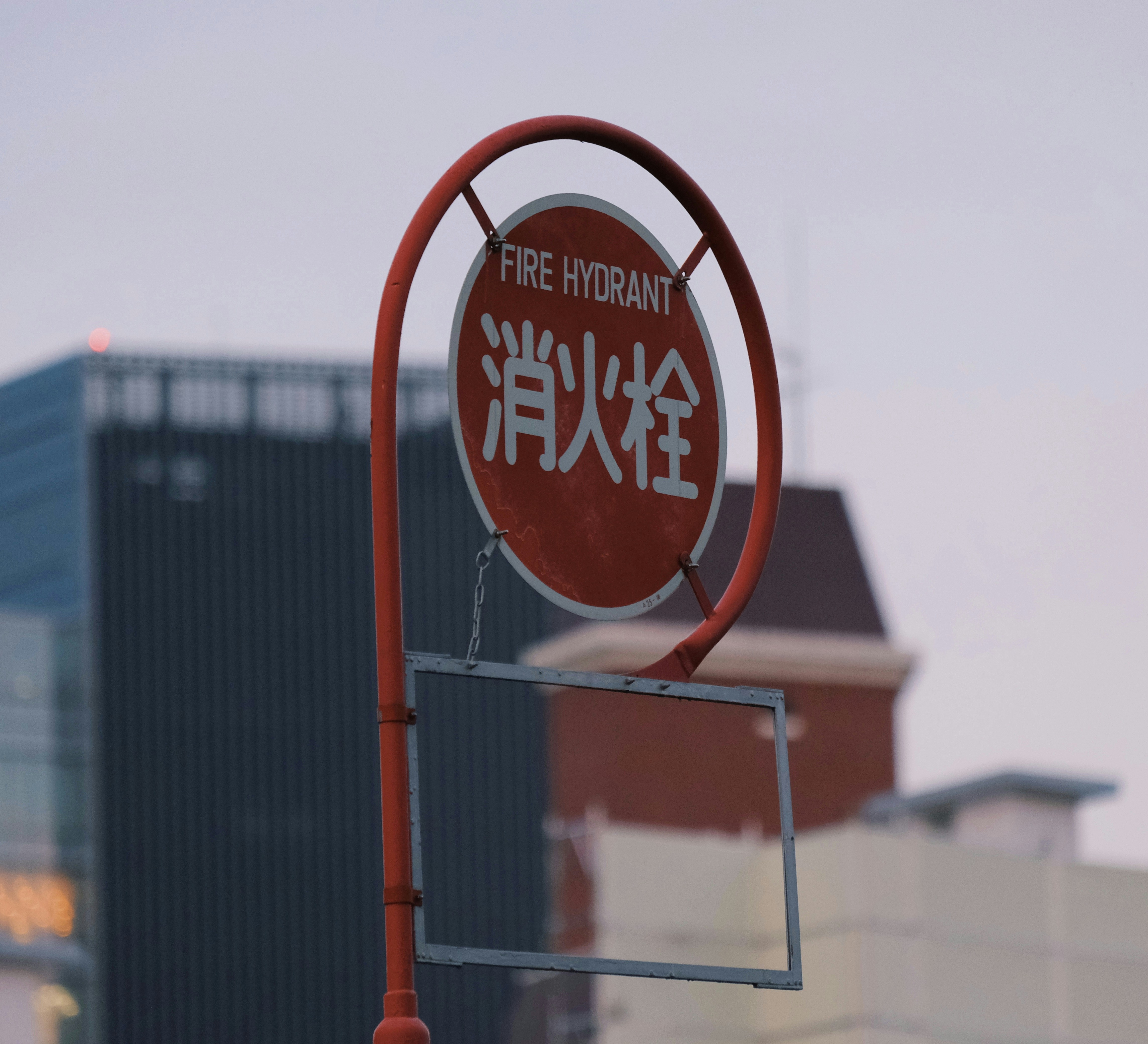 Red fire hydrant sign featuring both English and Chinese text against a blurred urban backdrop.