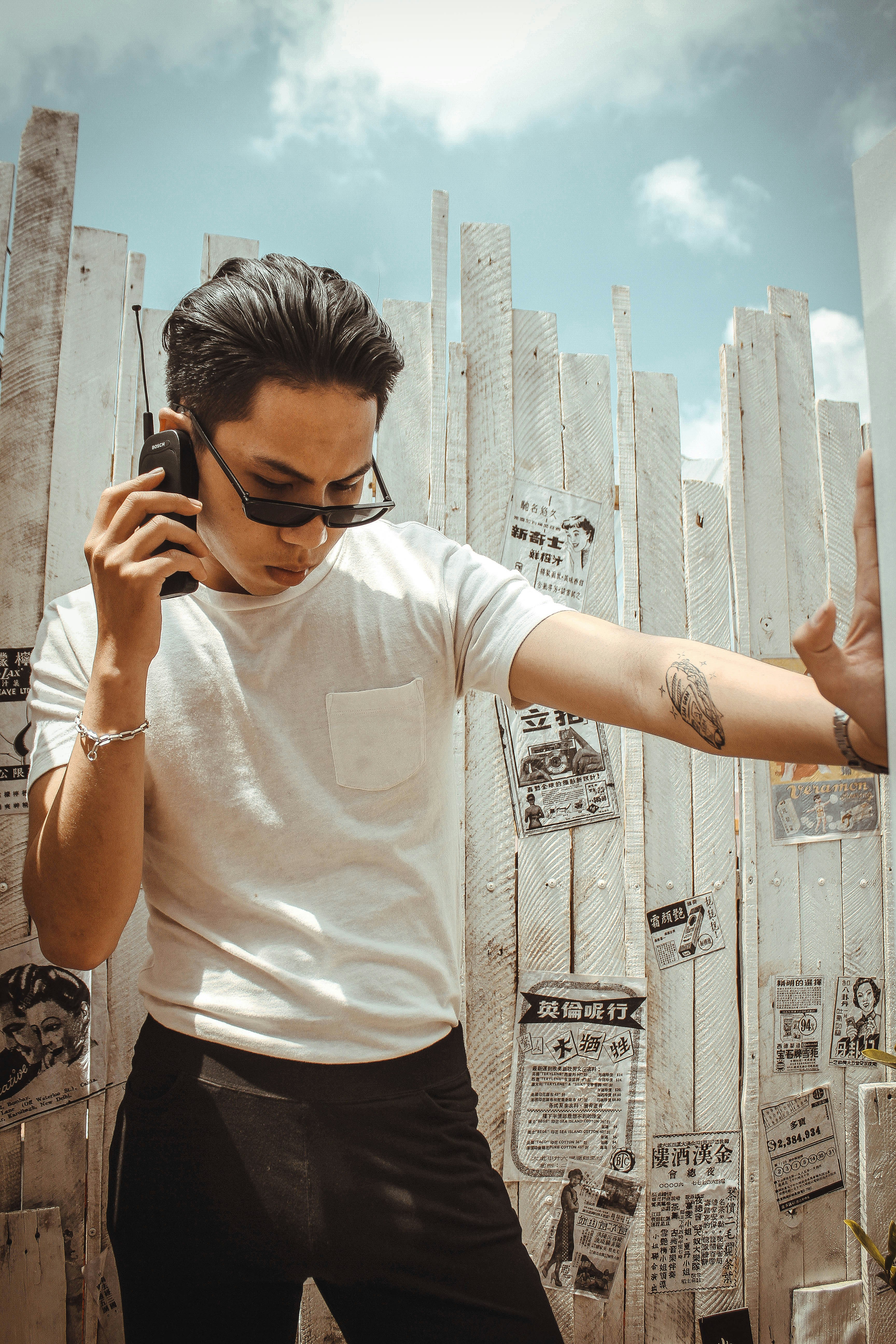 man in white crew neck t-shirt wearing black sunglasses holding black smartphone