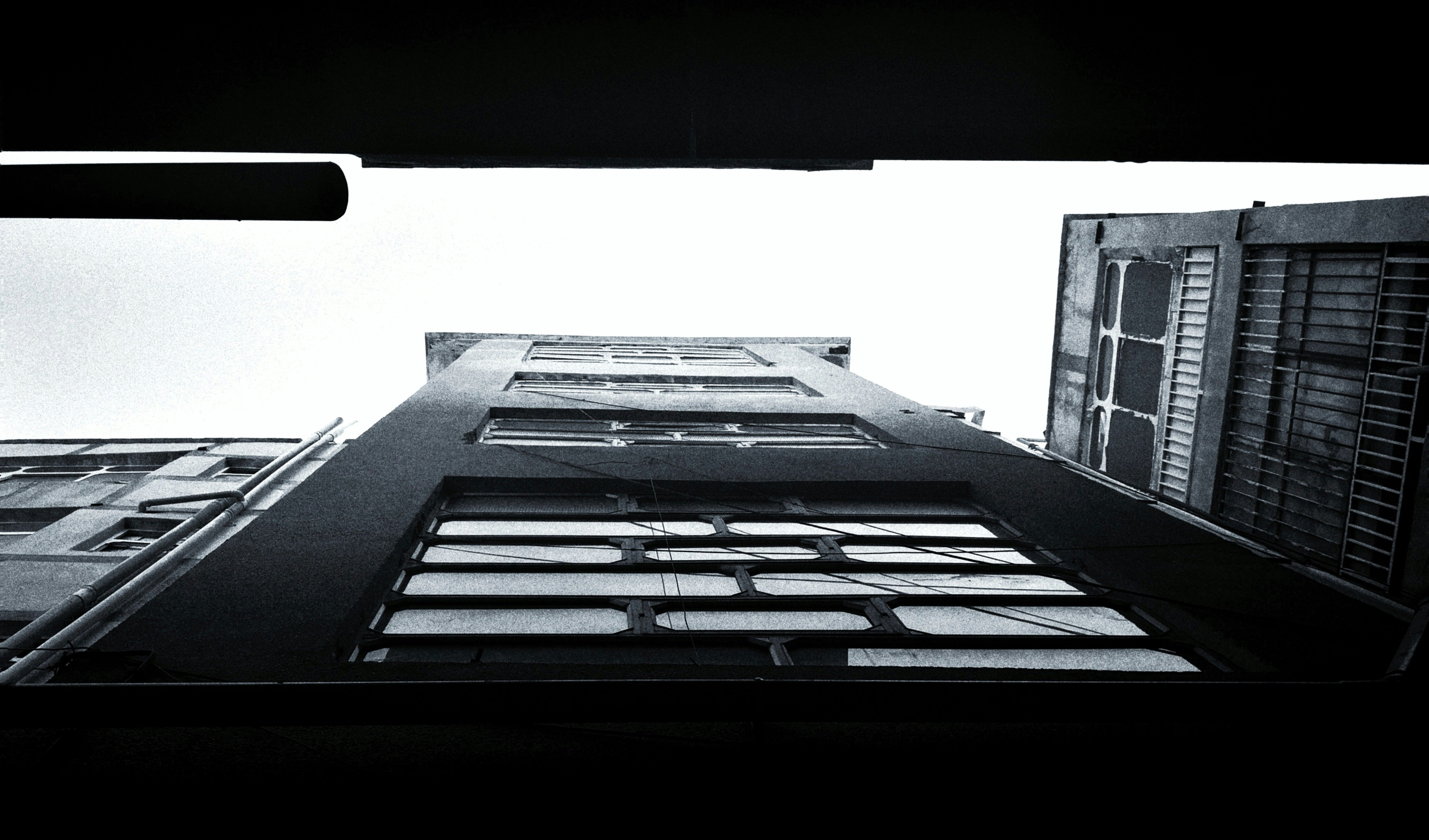 Looking up through a narrow alleyway flanked by towering buildings, showcasing a blend of modern and industrial architecture.
