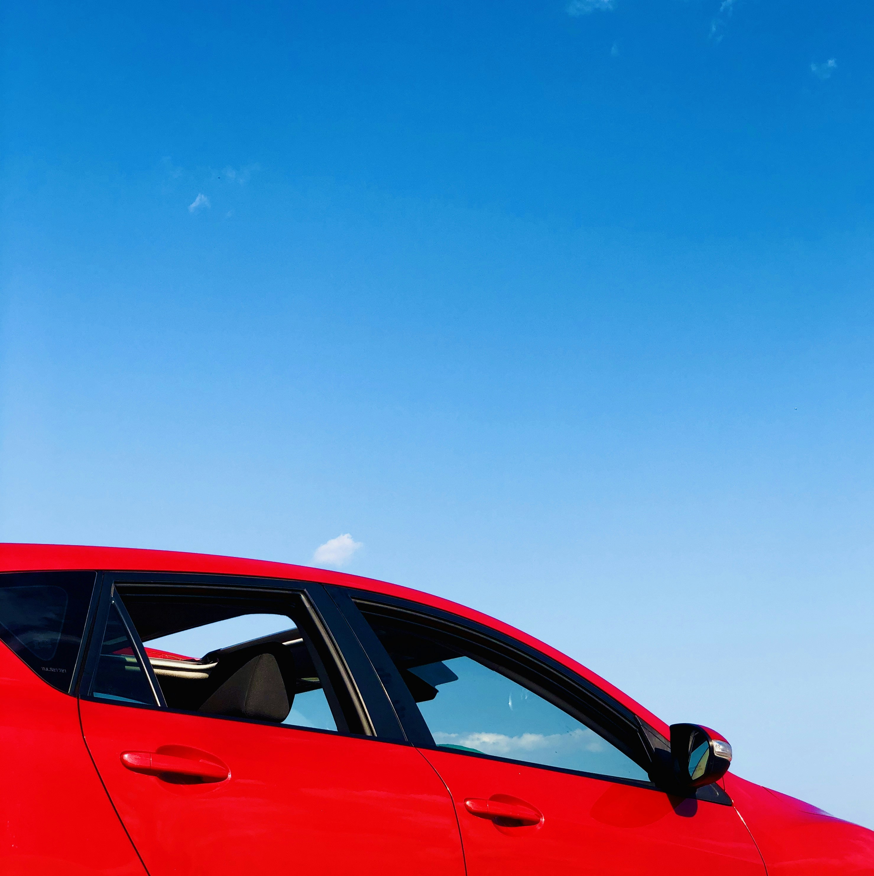 A sleek red car parked against a bright blue sky, emphasizing its modern design and vibrant color.