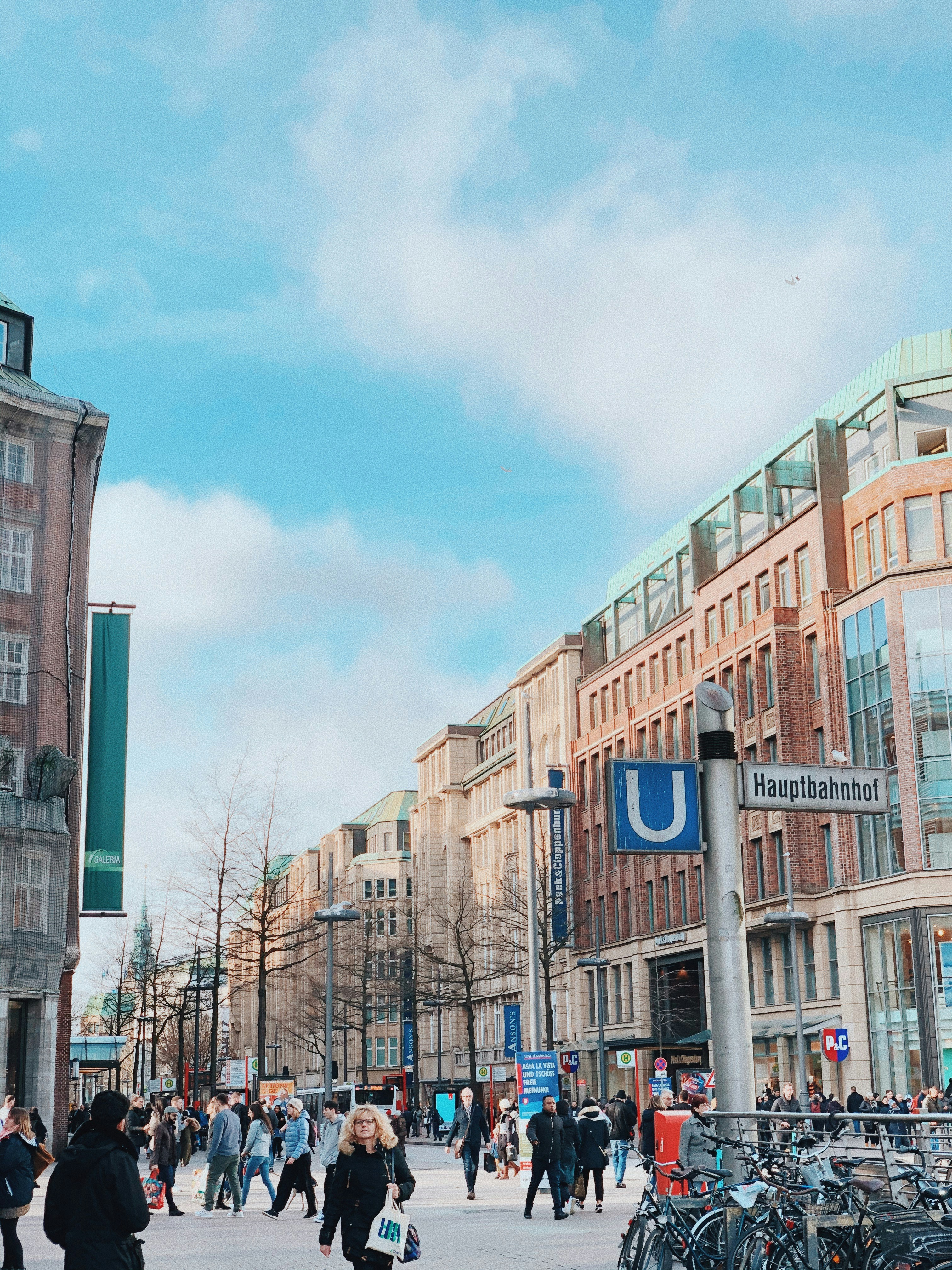 Bustling city square filled with pedestrians and modern architecture under a blue sky. Hauptbahnhof sign prominently displayed.