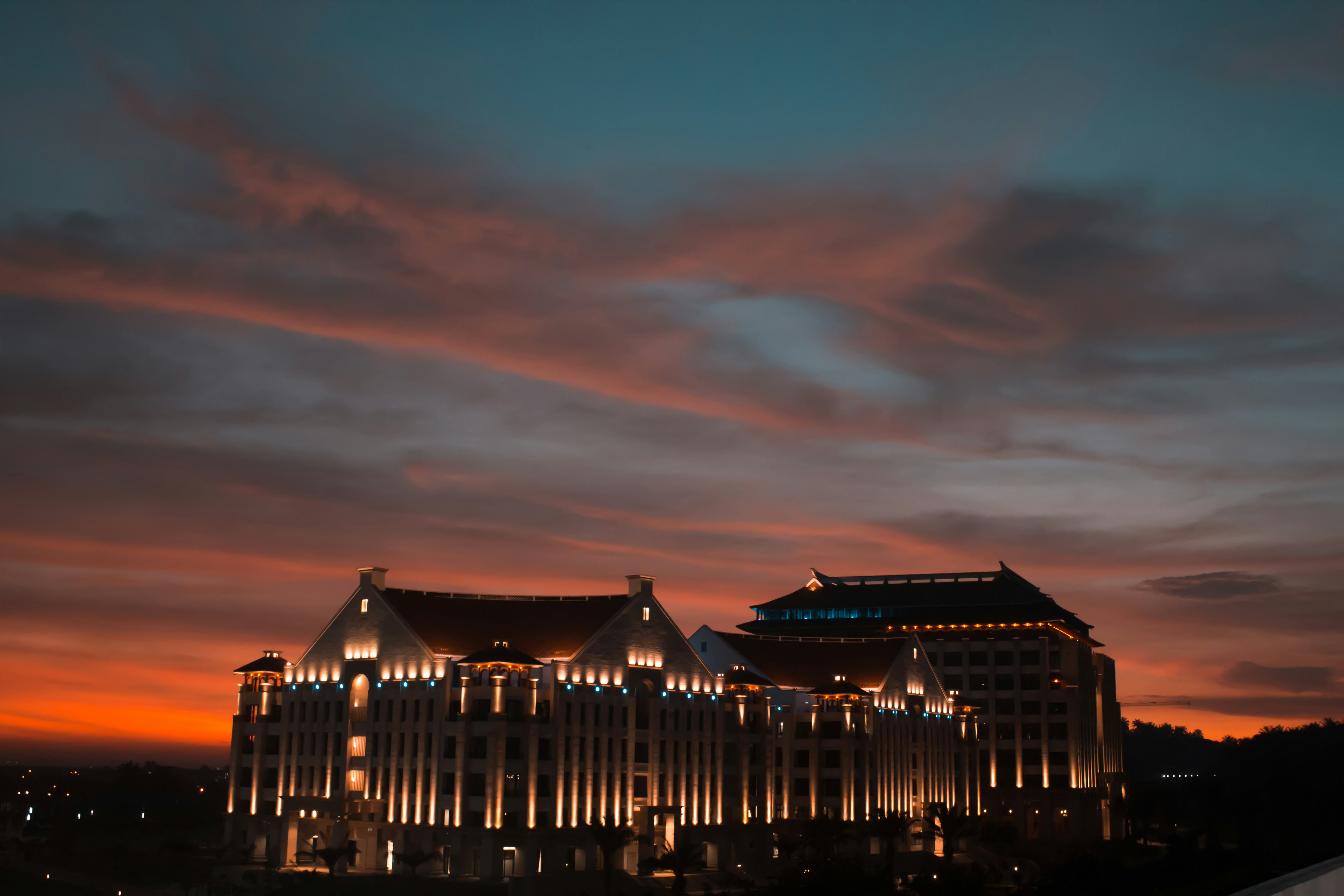 Illuminated building with intricate architecture set against a dramatic sunset sky with vibrant clouds.