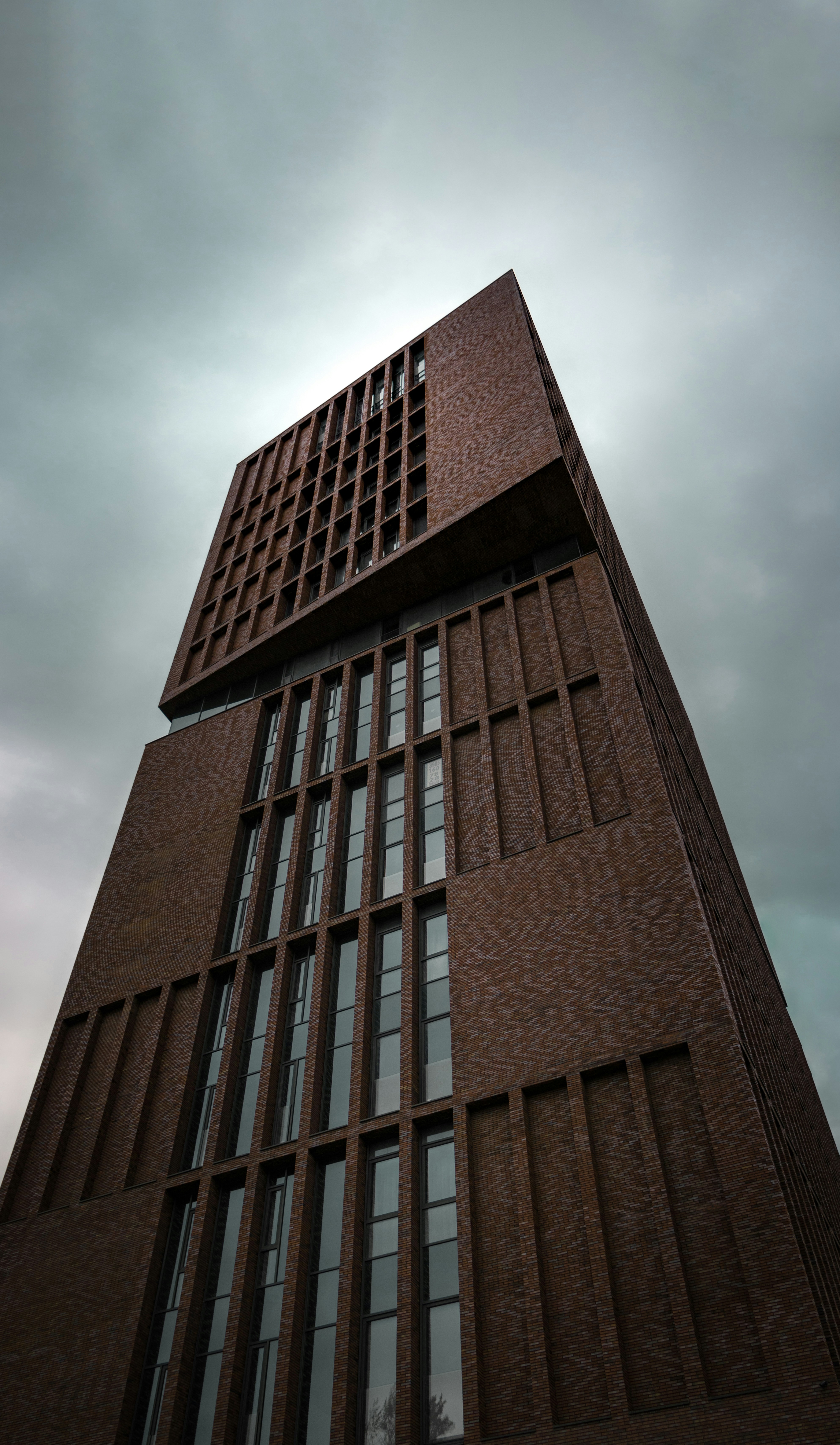 A striking modern tower constructed from rich brown bricks, rising dramatically against a cloudy sky.