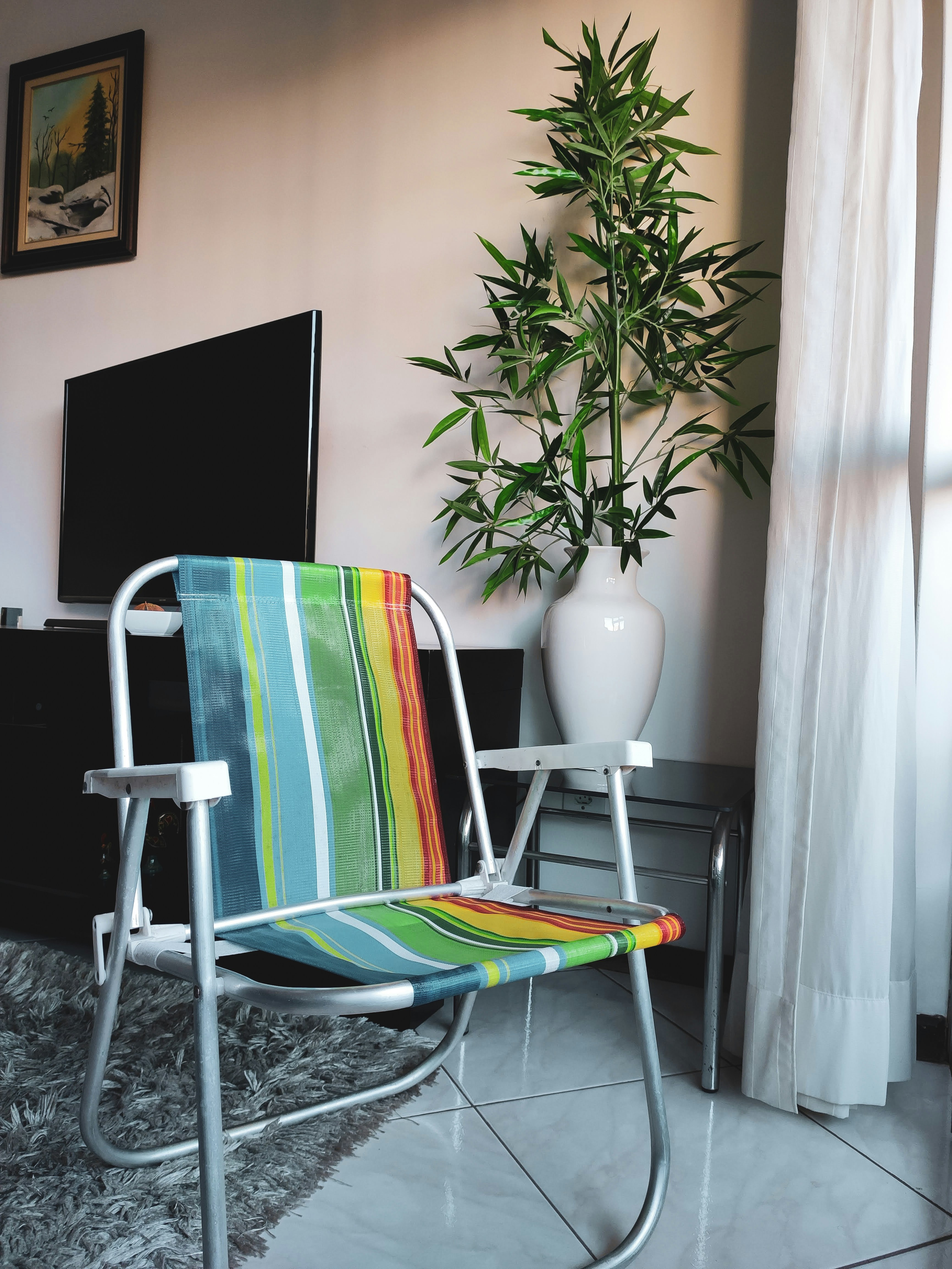 Striped beach chair placed in a living room next to a potted plant and a TV.