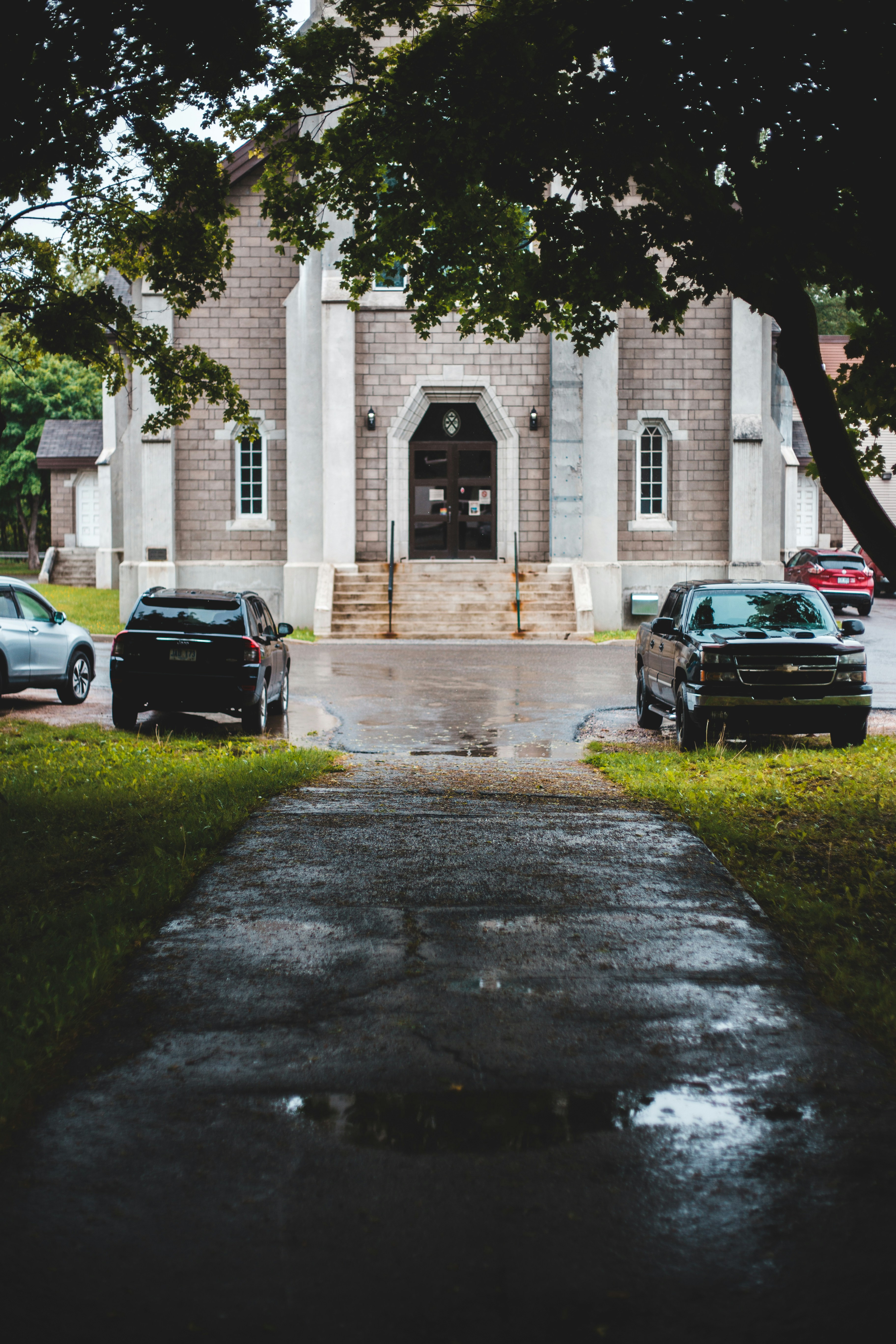 Central Church Entrance Framed by Rain-Soaked Drive and Shadowed Trees