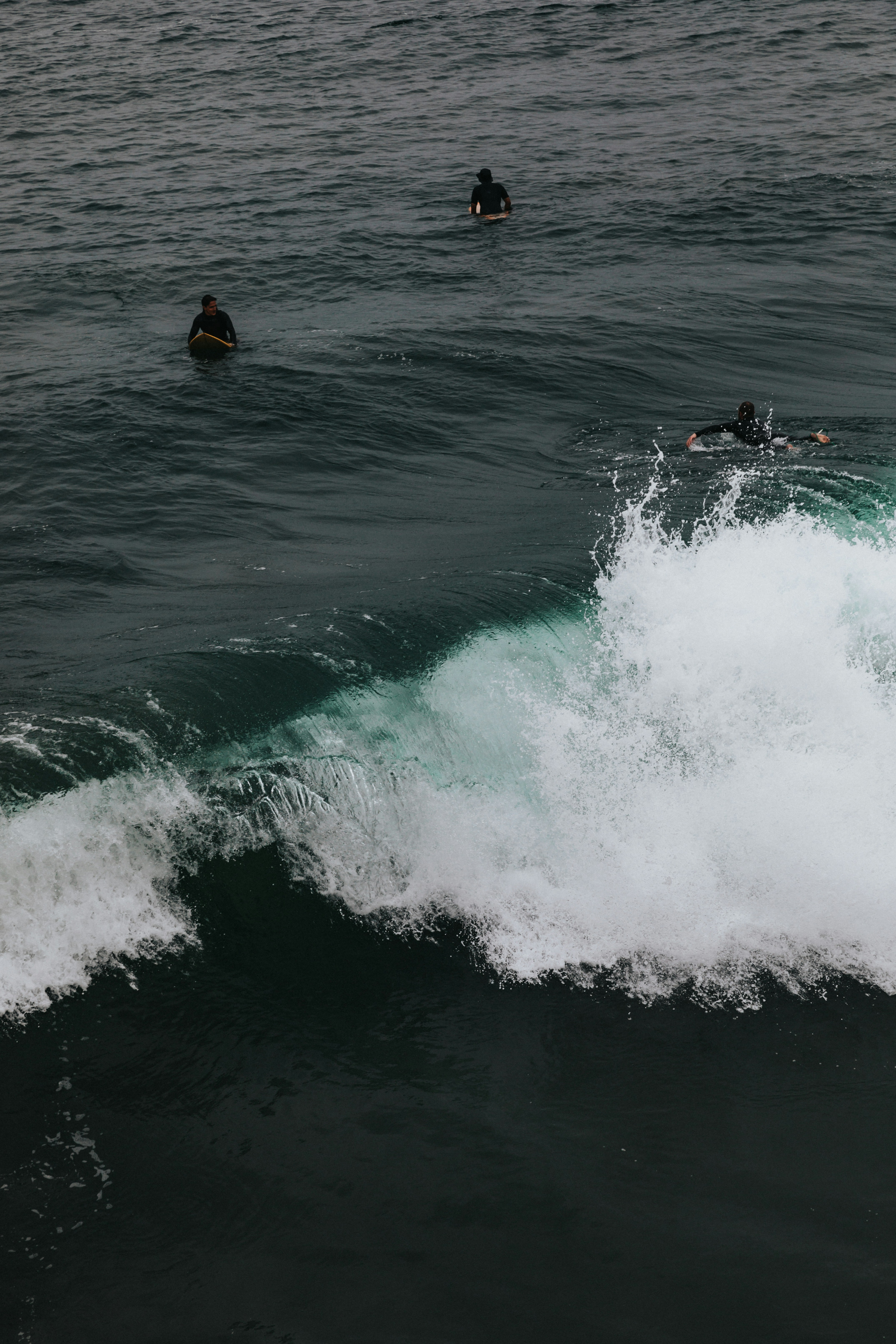 Surfers waiting in the ocean, poised for the next wave, as a crashing wave creates a frothy display. The scene captures the thrill of surfing in dynamic waters.