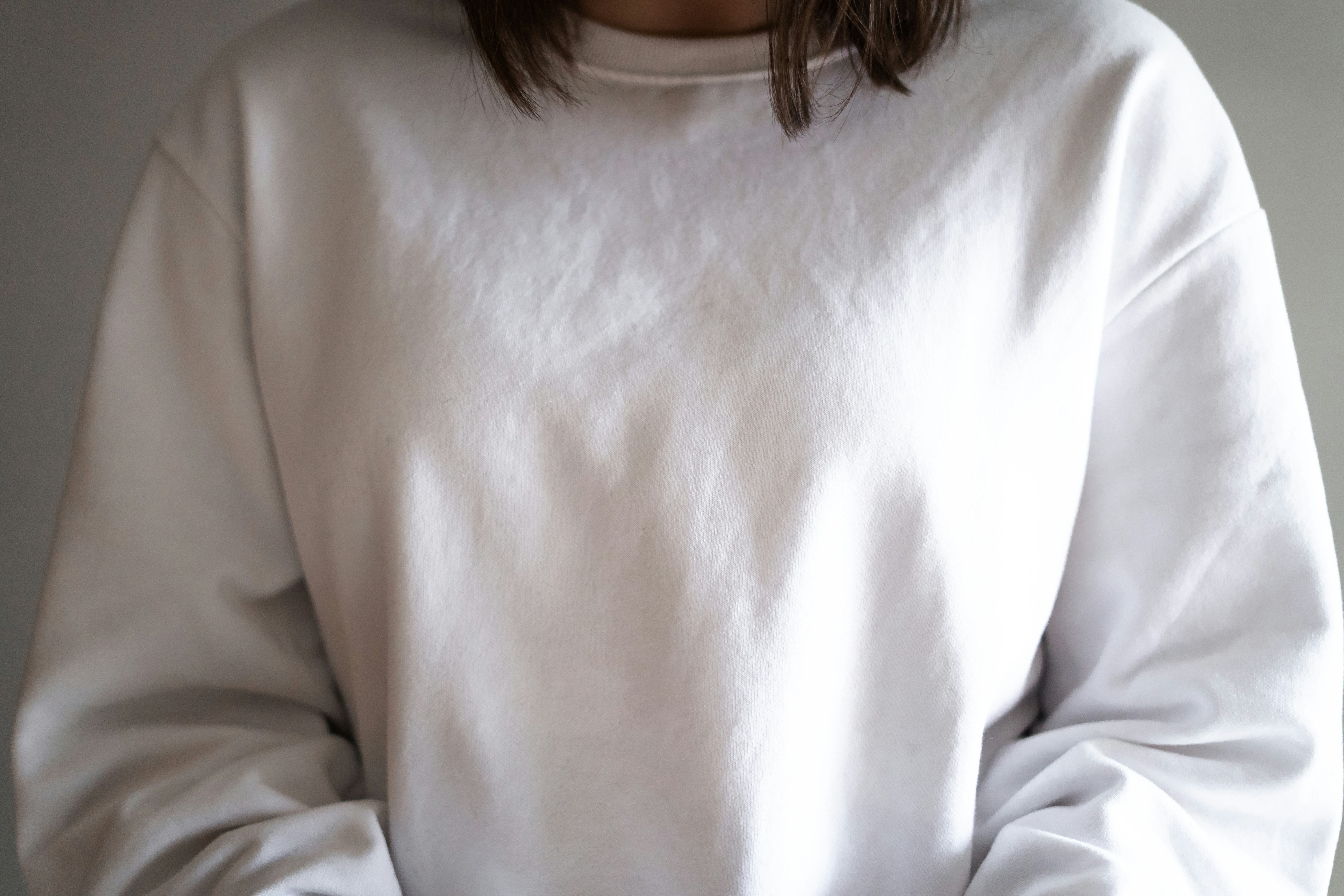 A person in a cozy white sweatshirt, hands clasped in front, exuding a sense of calm and simplicity.