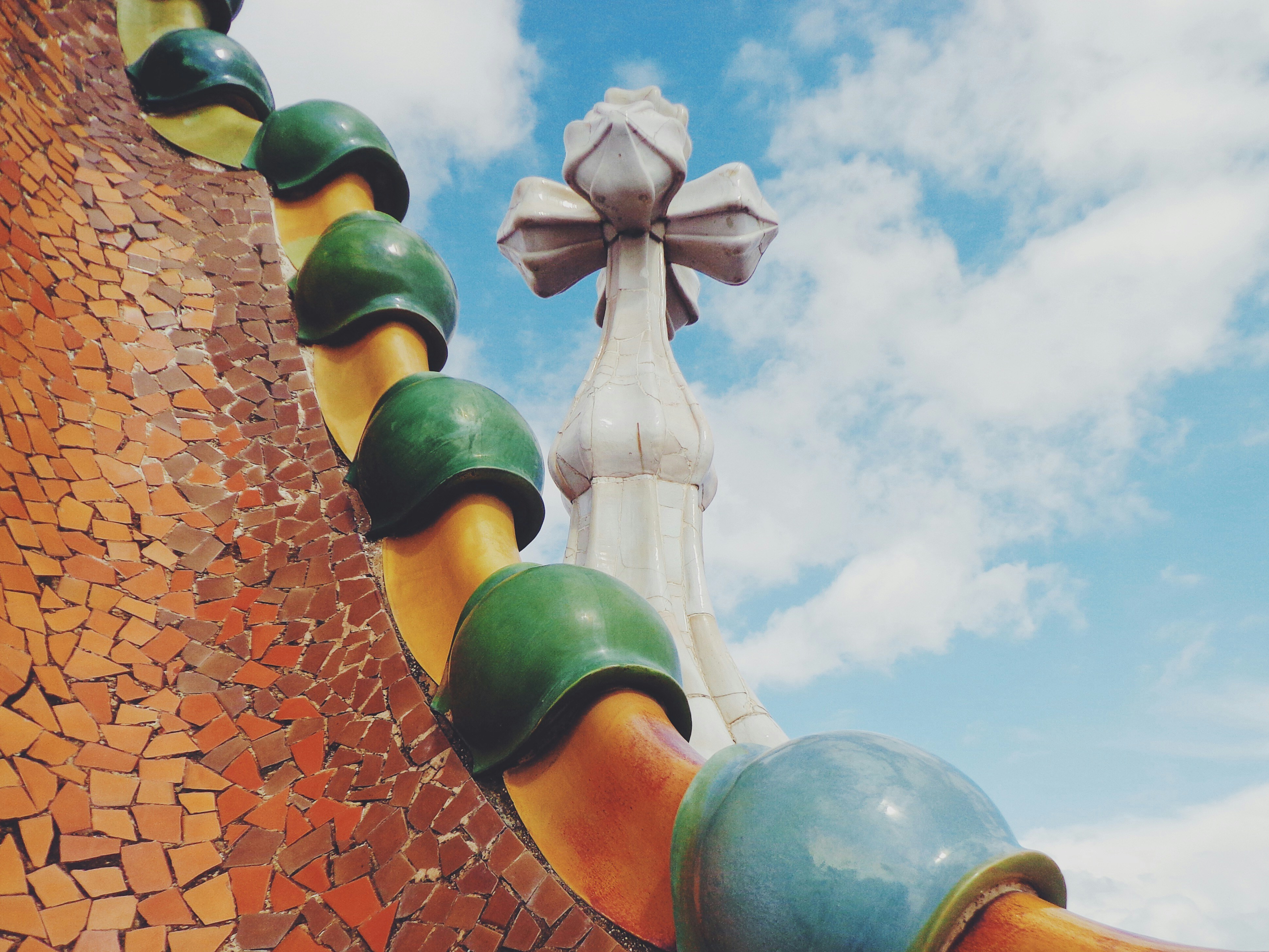Colorful ceramic tiles and green bulbous forms on Gaudí's Casa Batlló rooftop against a cloudy sky.