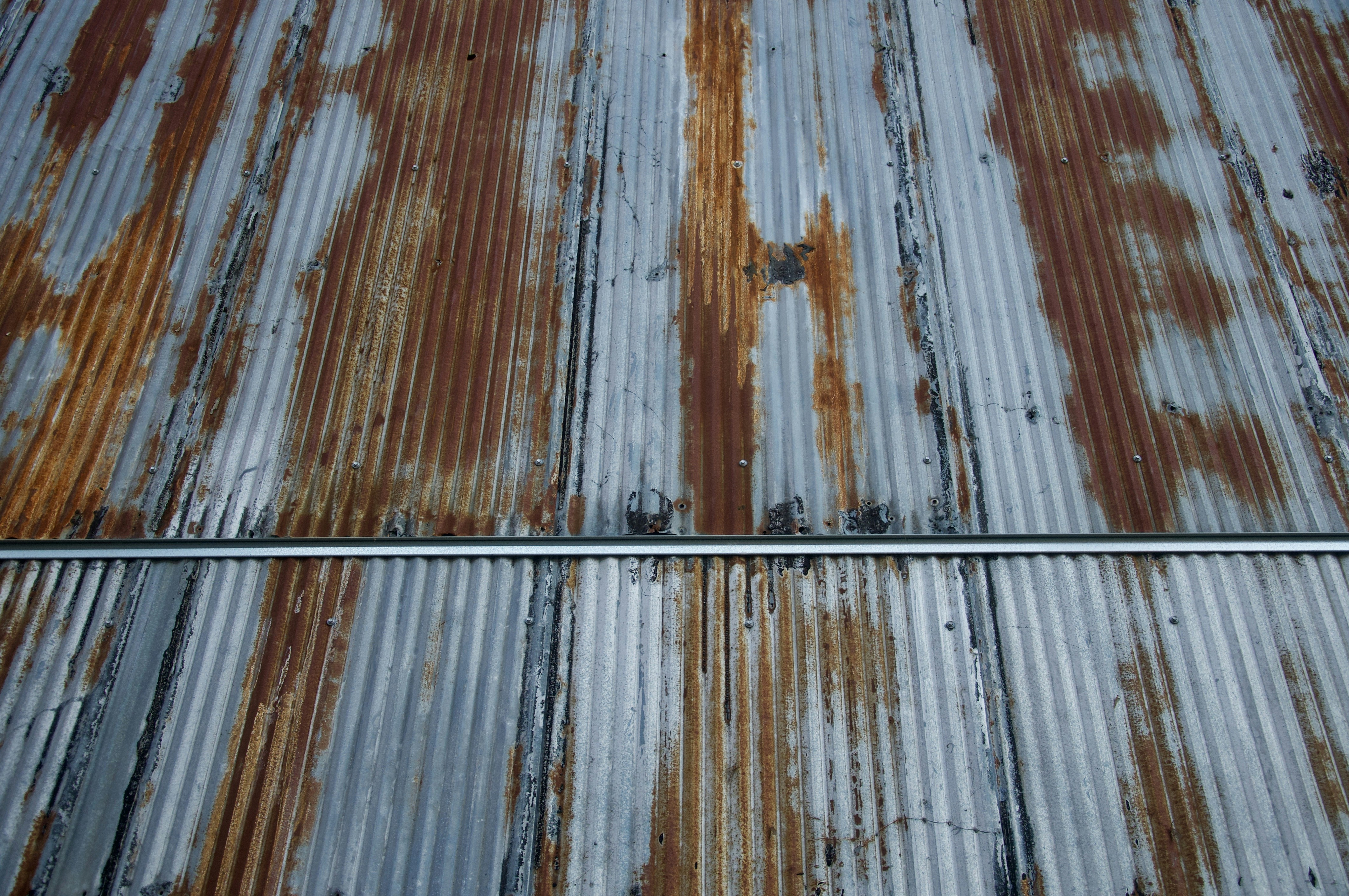 Close-up of a corrugated metal roof showcasing rust patterns and weathered textures. The interplay of colors illustrates the passage of time.