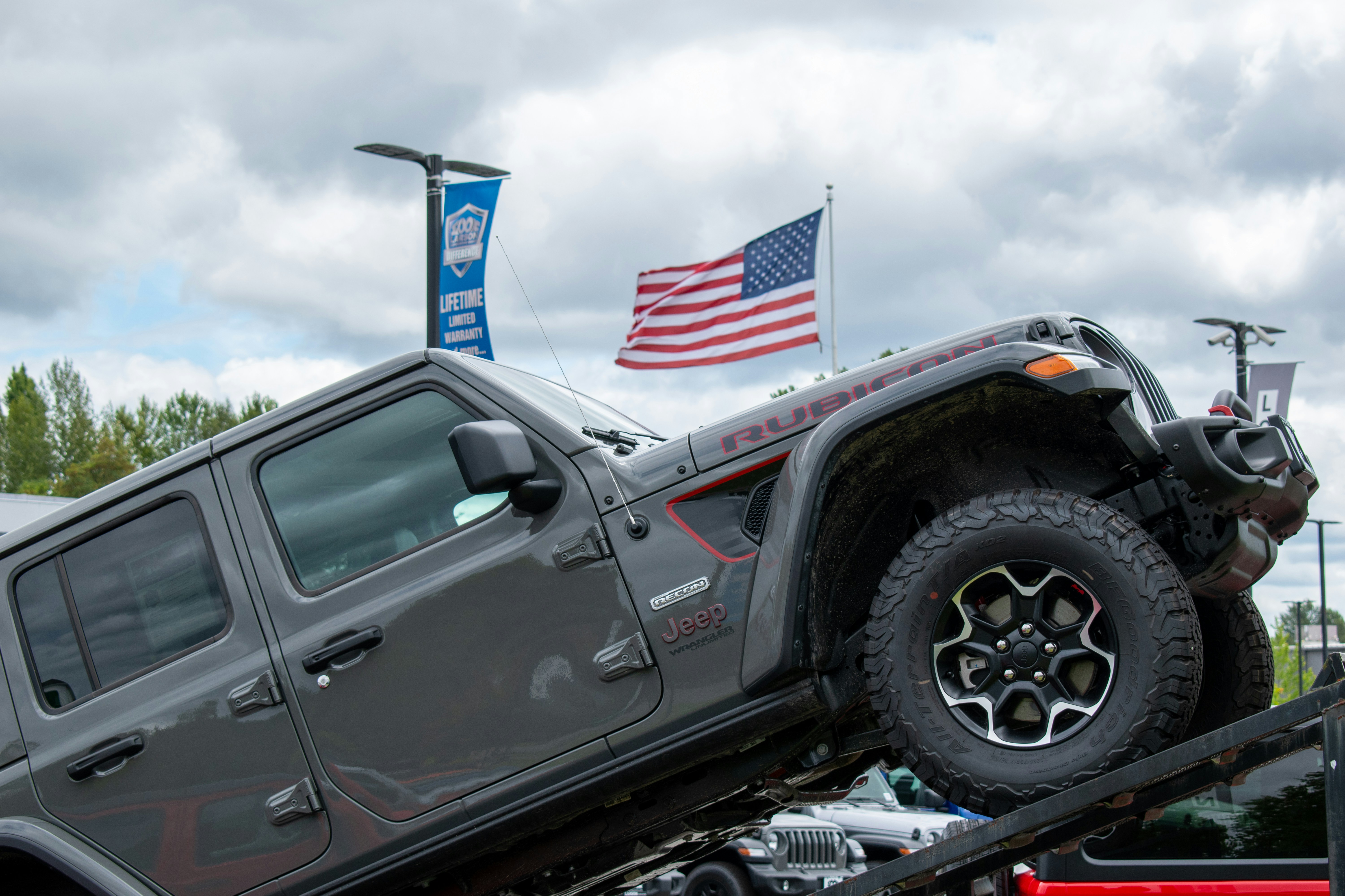 Black Chevrolet crew cab pickup truck with a US flag on top, angled on a ramp under a cloudy sky.