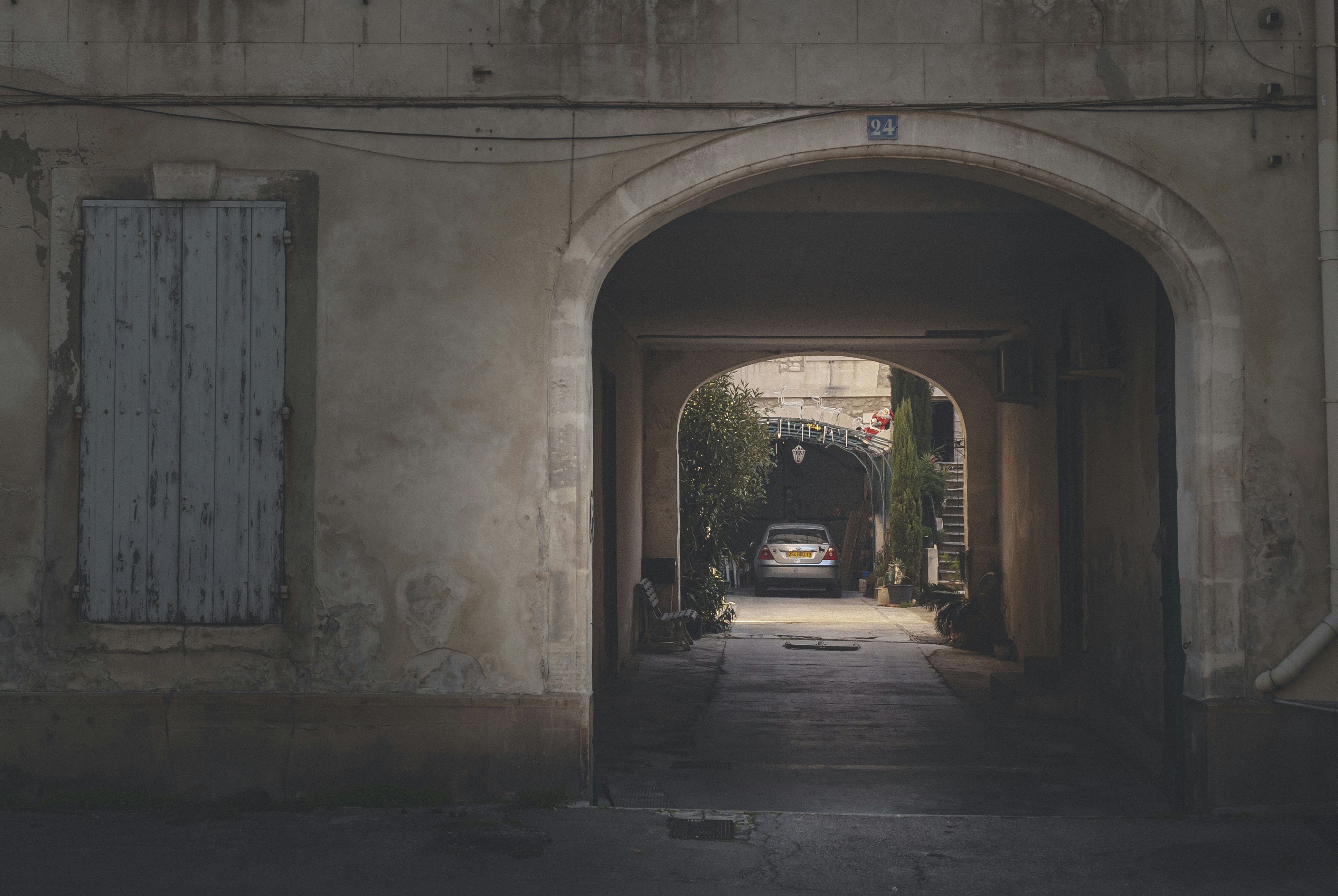 A narrow archway reveals a glimpse of a parked car in a secluded courtyard, framed by weathered walls and soft greenery.