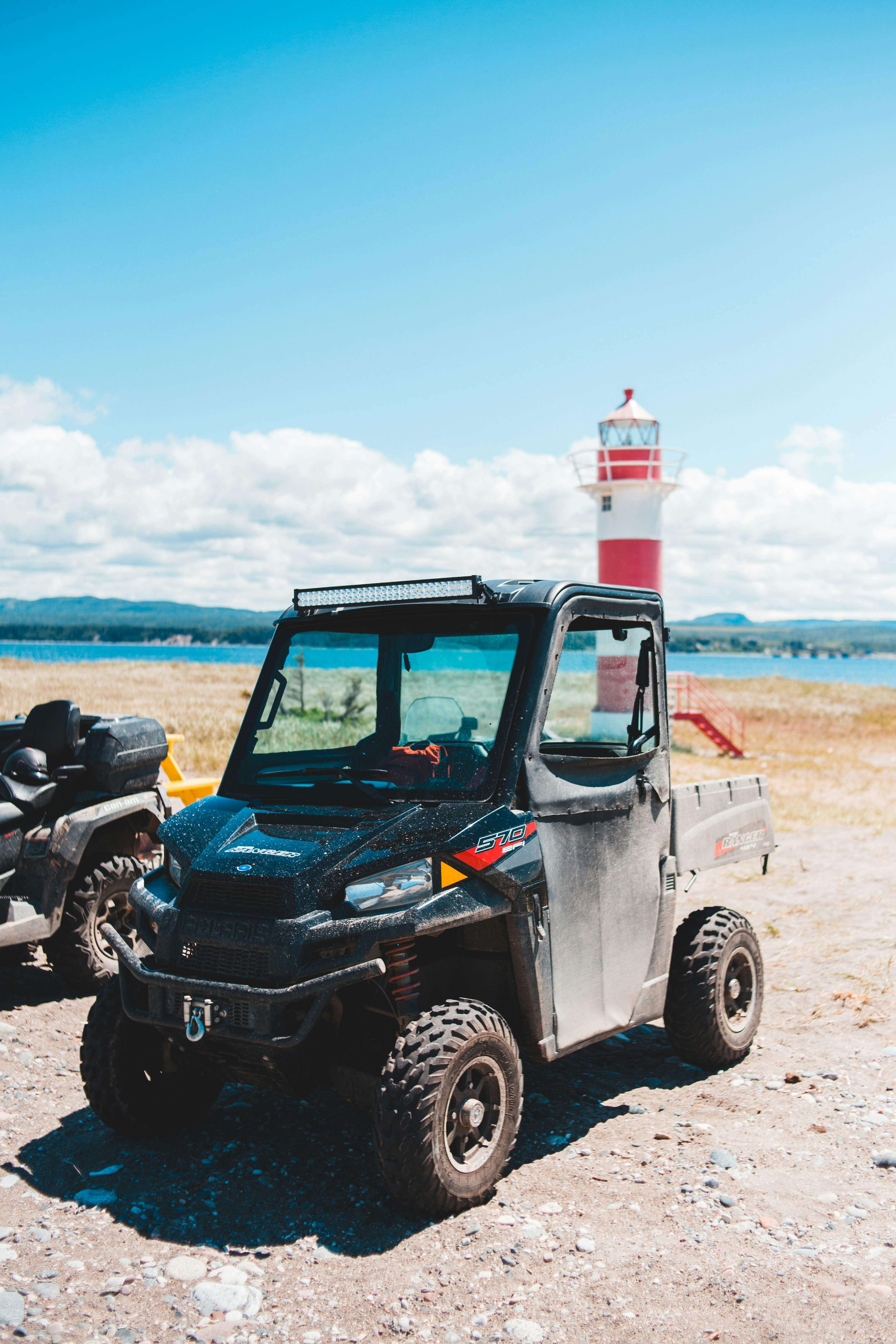 Off-road Echoes: A Utility Vehicle Beside a Red-White Lighthouse