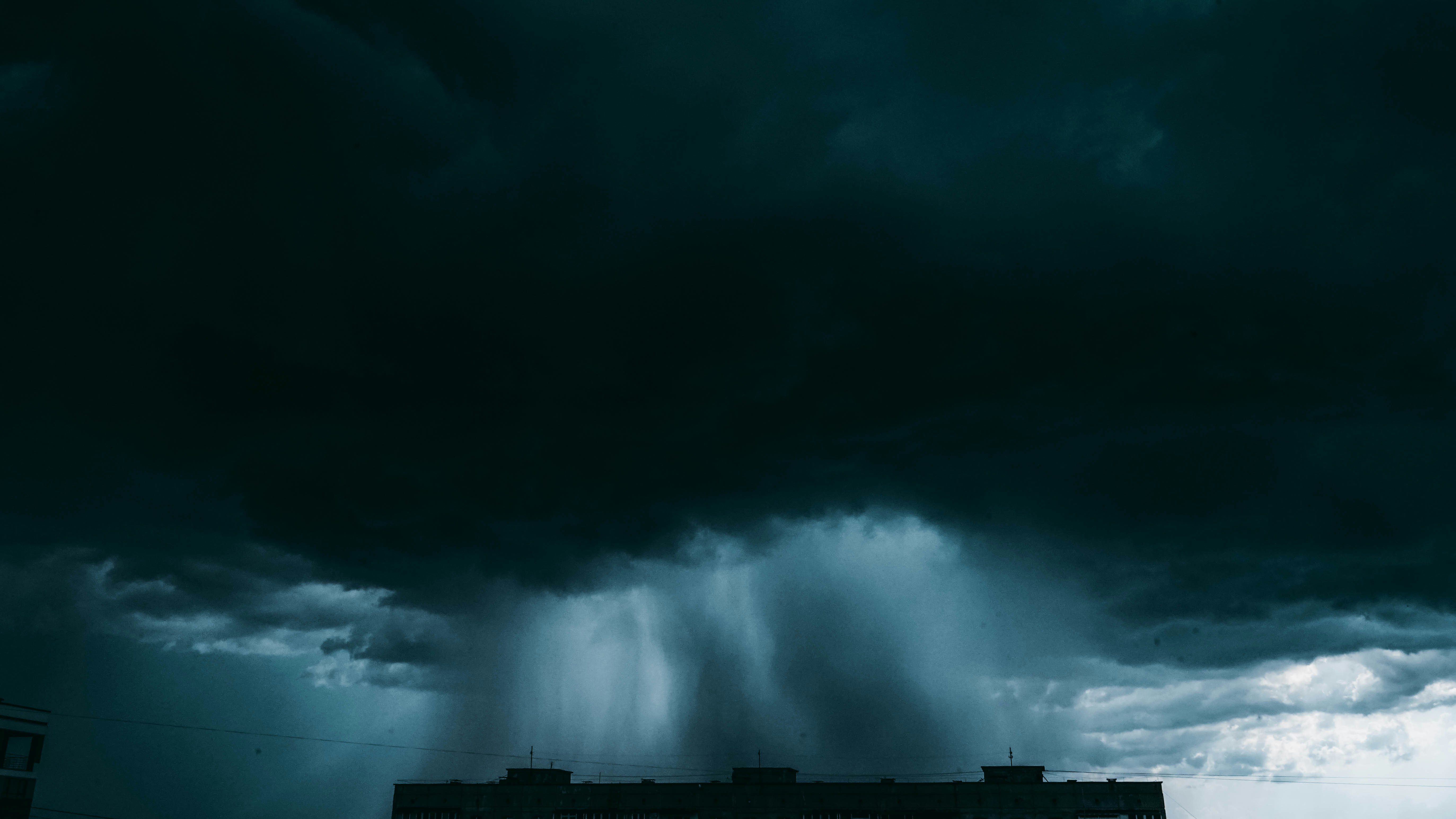 Dark storm clouds loom over city buildings at night, with patches of lighter clouds creating dramatic contrast.