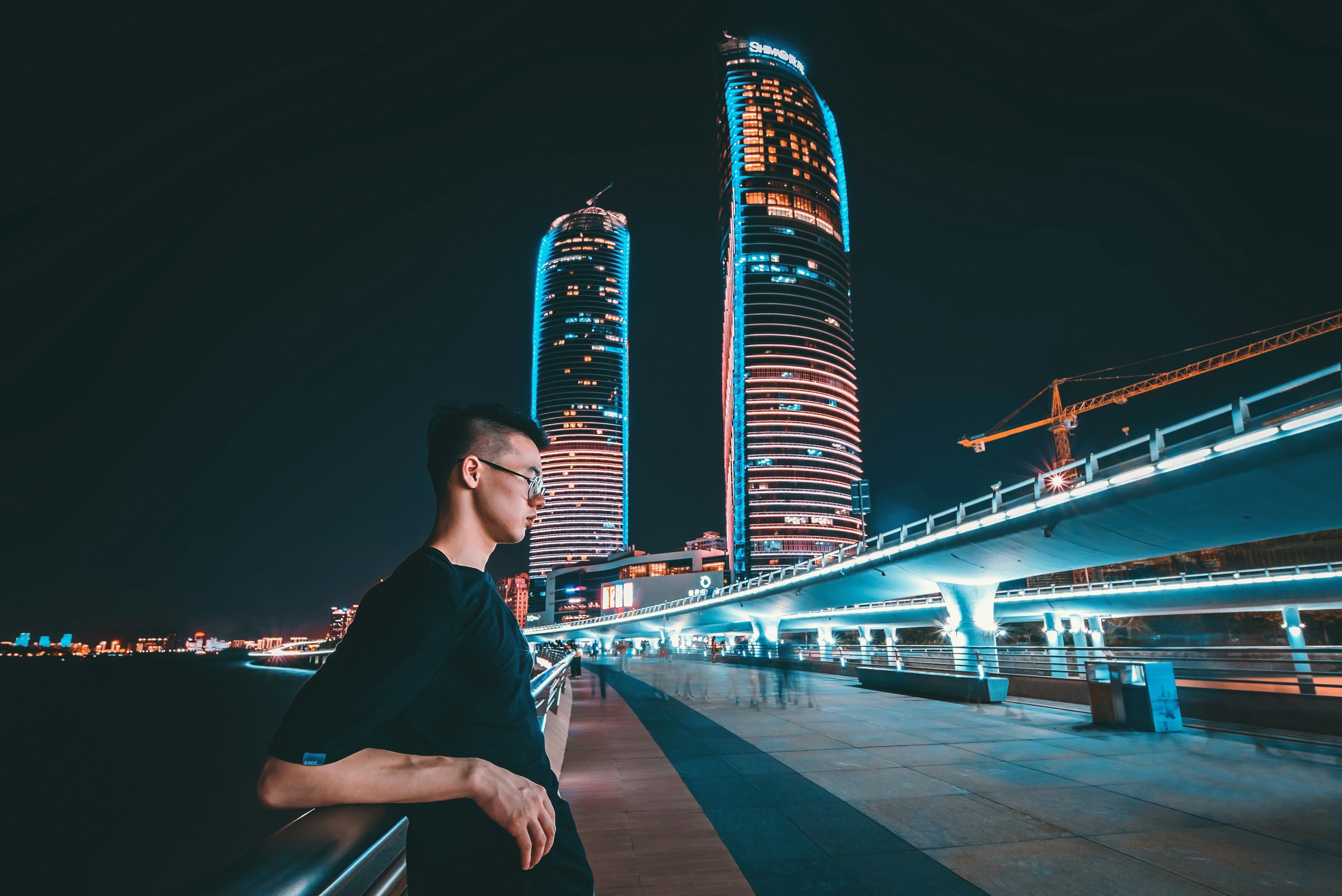Person standing on a walkway gazing at illuminated twin skyscrapers against a night sky.